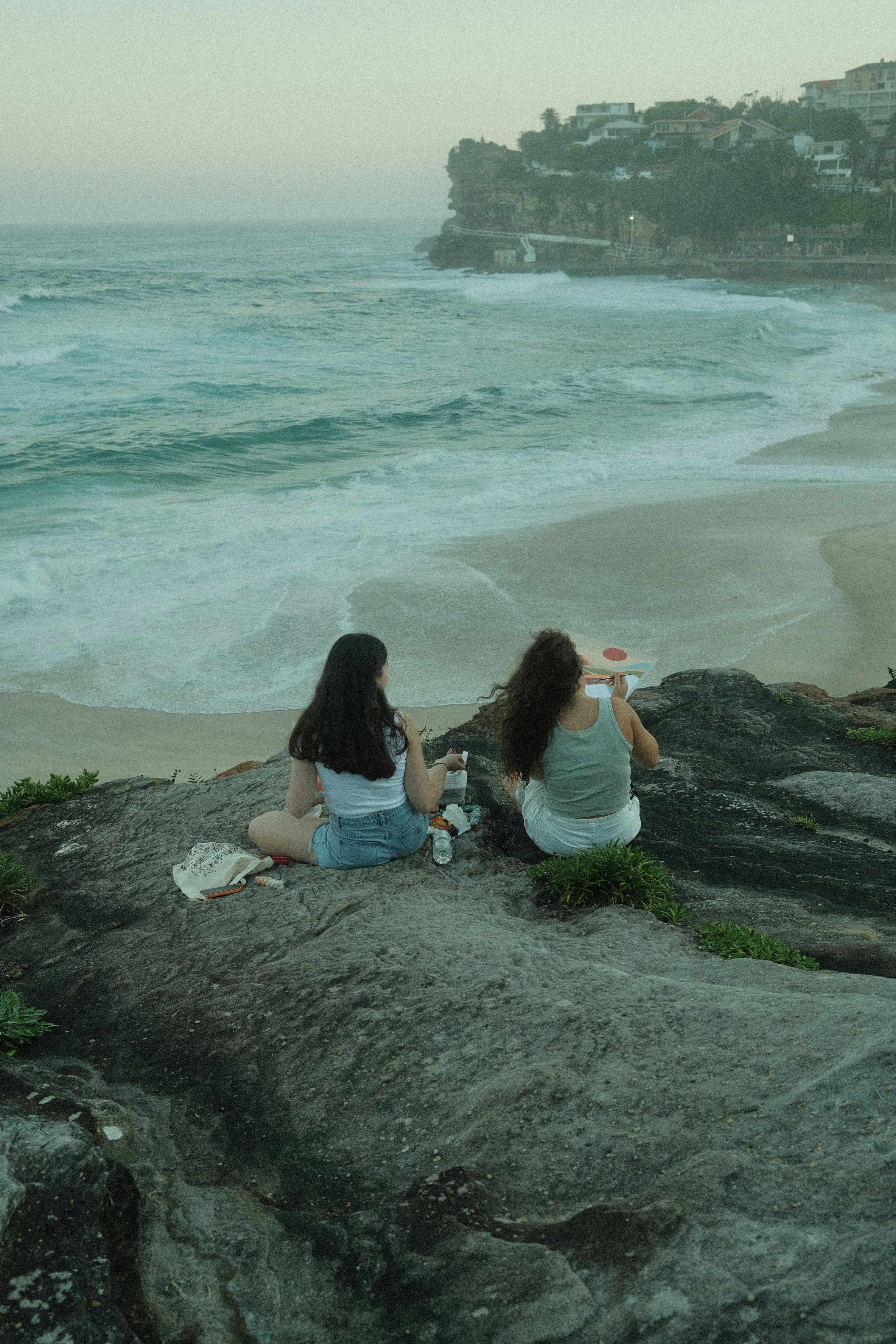 two women sitting on a rock overlooking the ocean