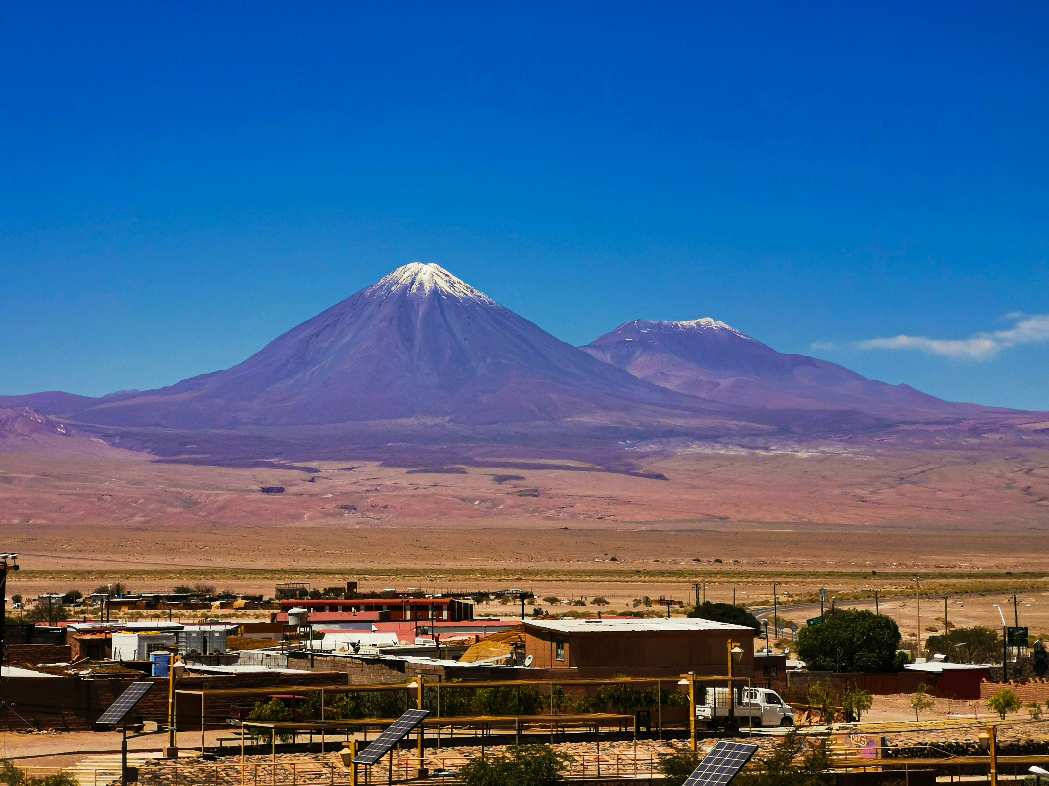 Majestic twin volcanoes rise above the arid landscape, framed by a clear blue sky and dotted with small settlements below.