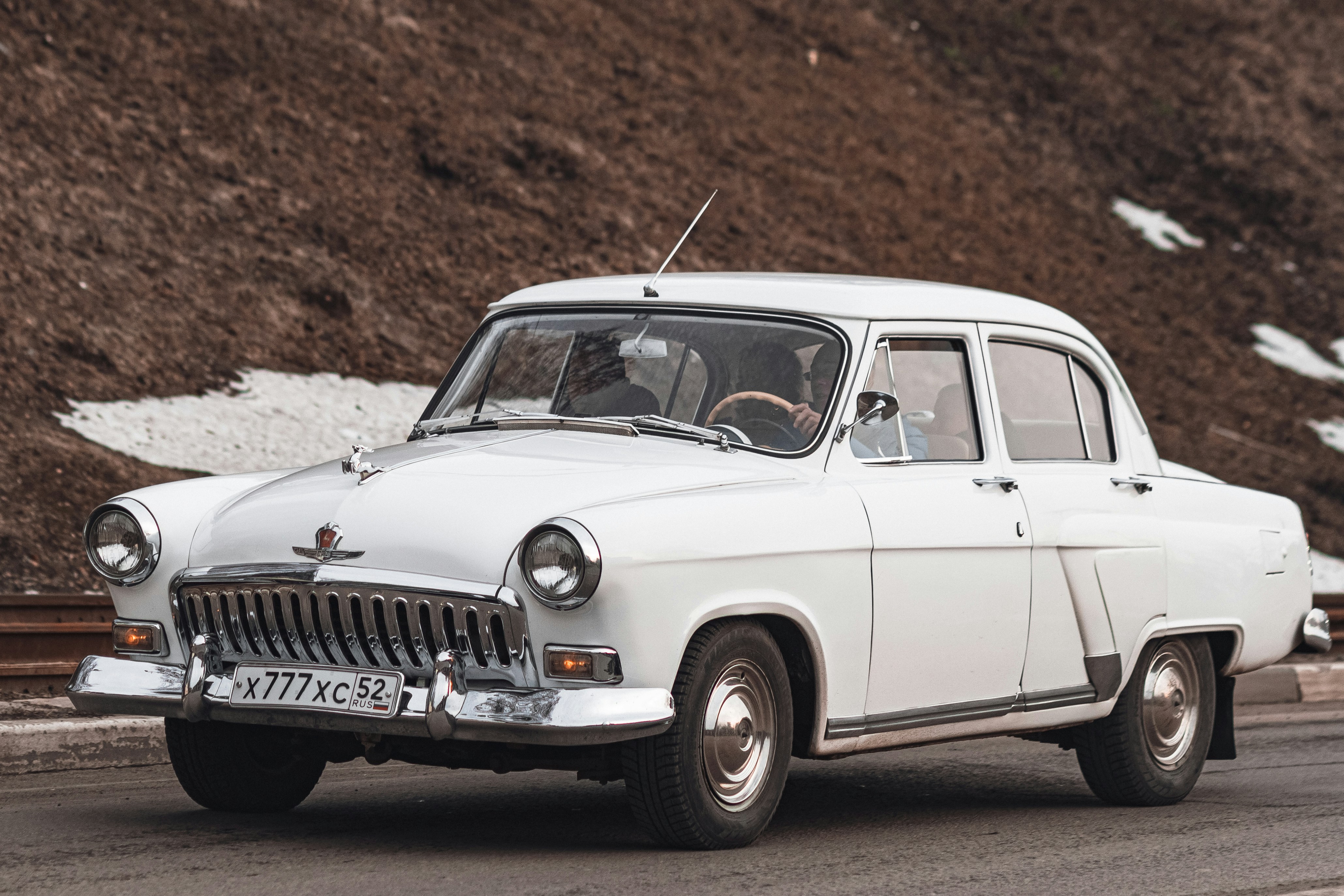 Vintage 1950s white sedan gliding along a sunlit hillside road
