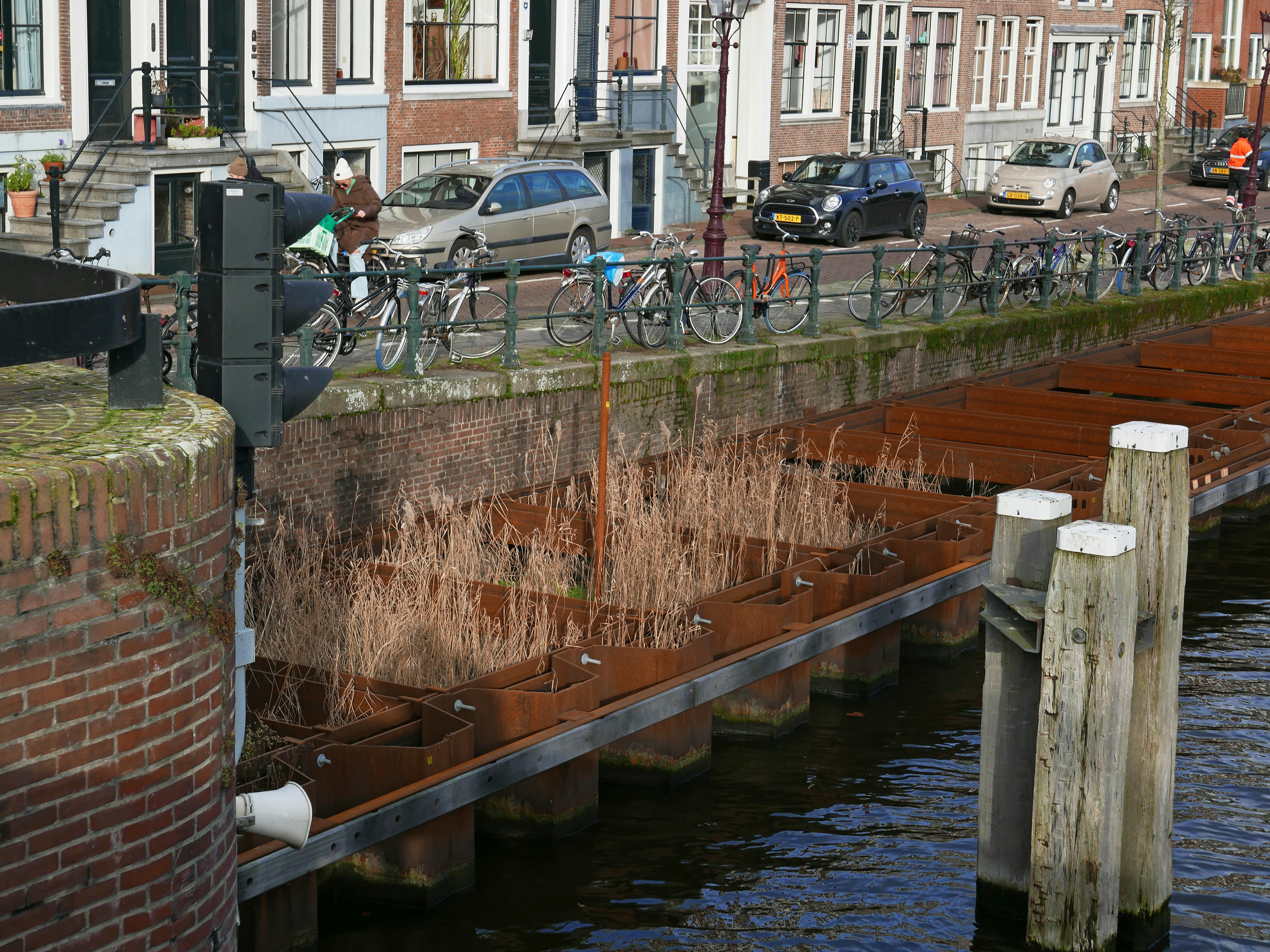 Rustic canal-side view featuring a row of bicycles and a stark contrast between natural and urban elements. The scene captures the essence of city life intertwined with nature.