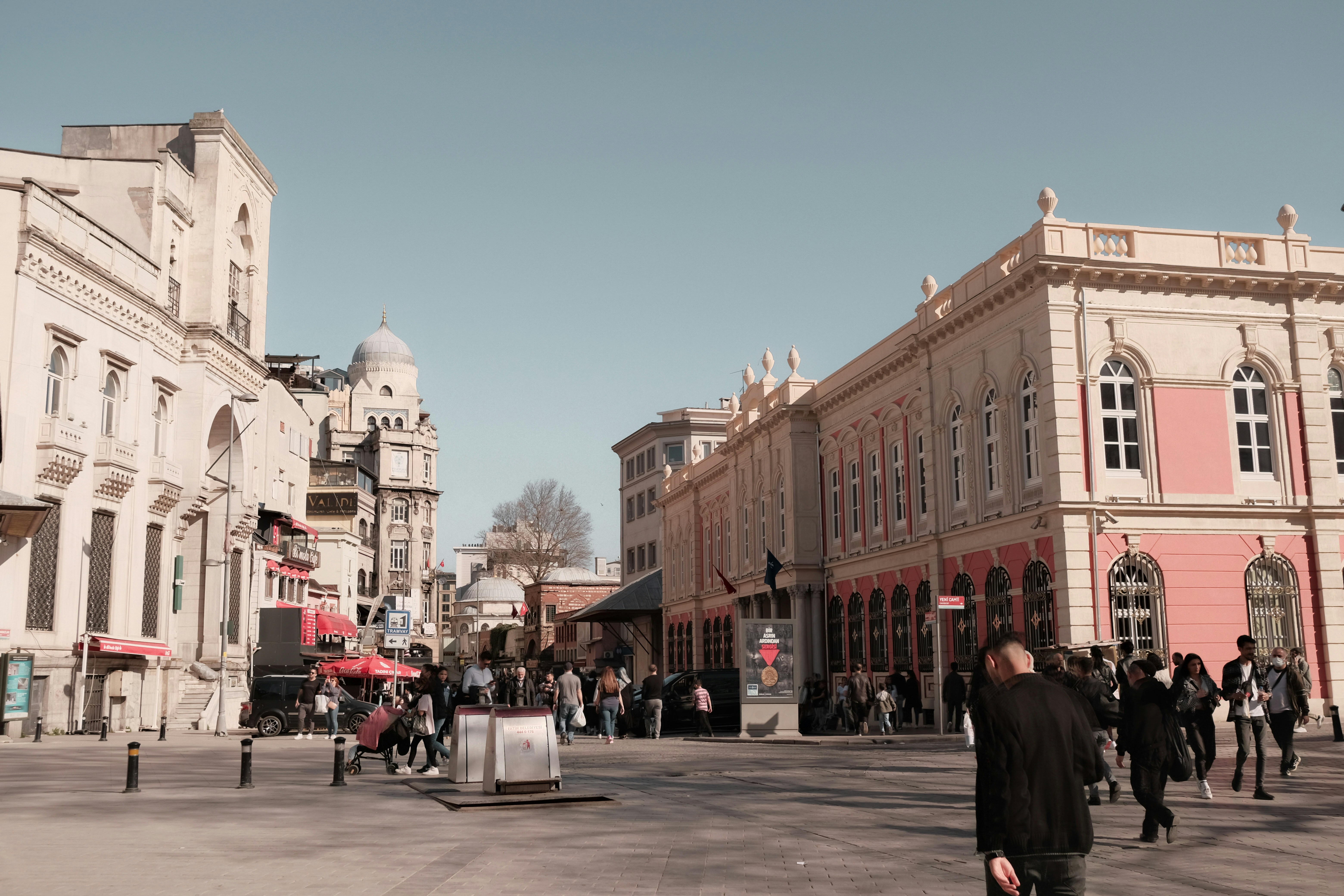 Vibrant city square bustling with pedestrians and historic architecture, featuring a blend of modern and classic buildings. The scene captures the essence of urban life.