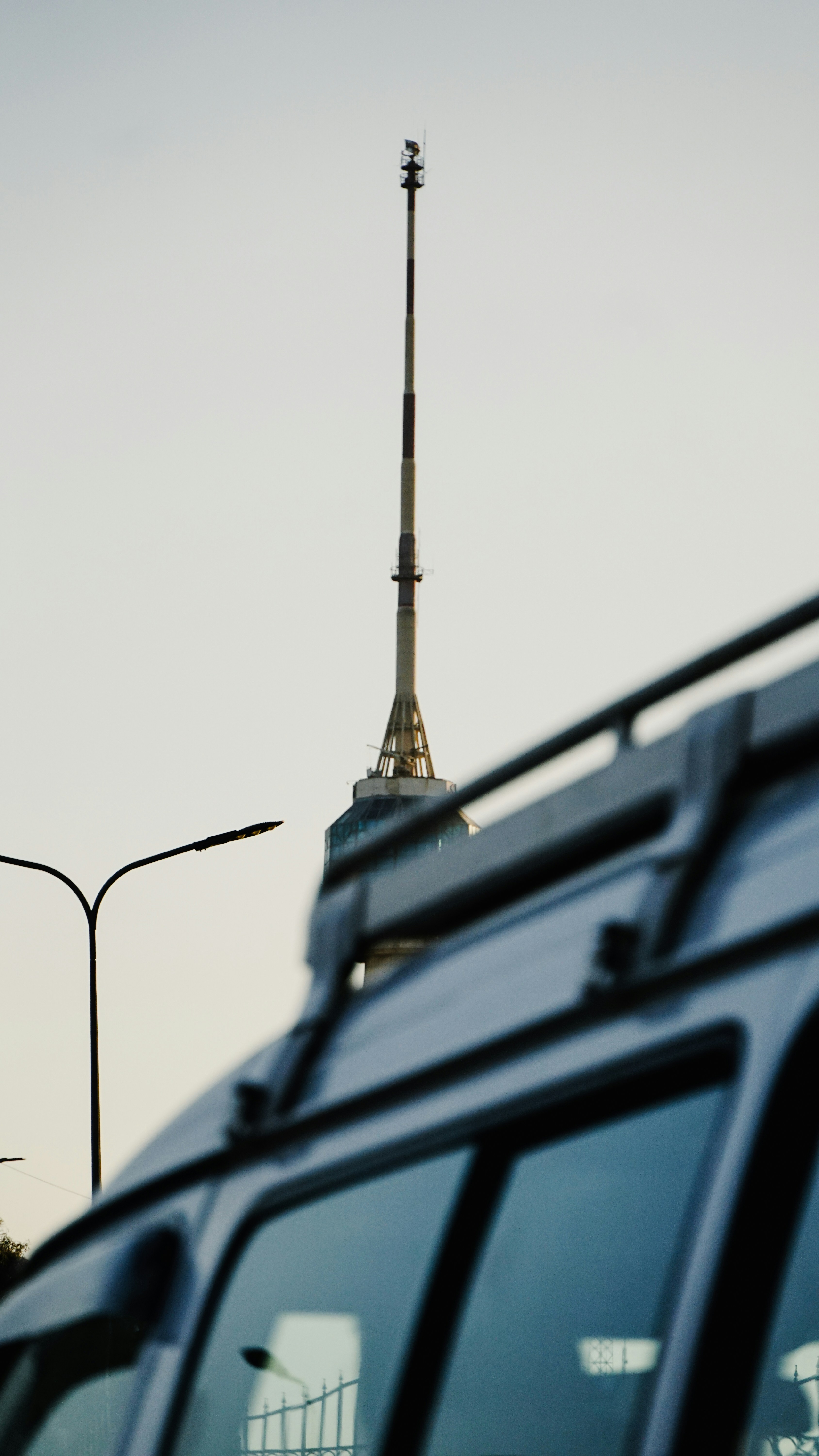 Vertical Signal: A Tower Pierces a Quiet Sky Behind a Framed Vehicle