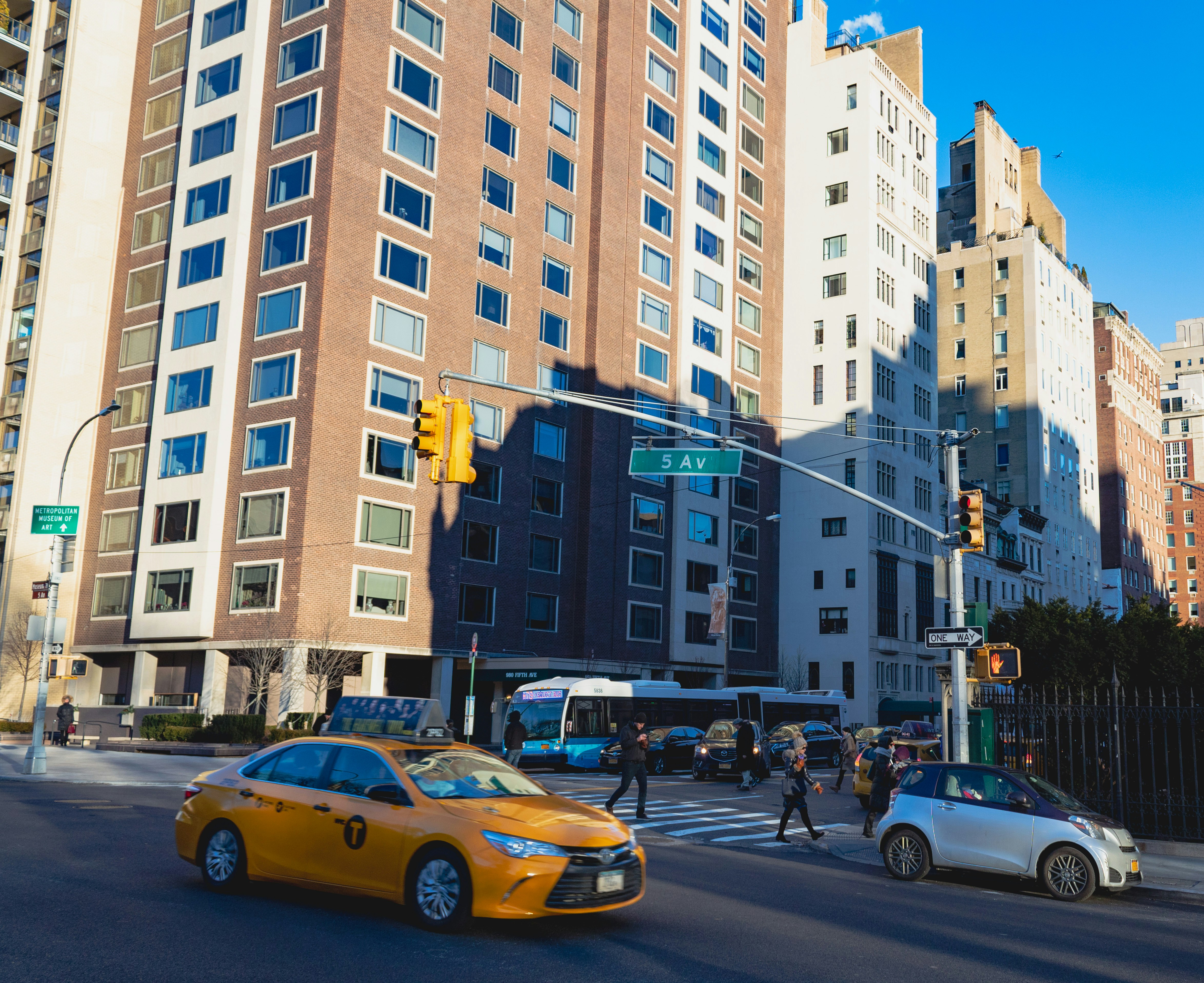 A bustling city intersection showcasing a yellow taxi, pedestrians, and modern buildings under a clear blue sky.