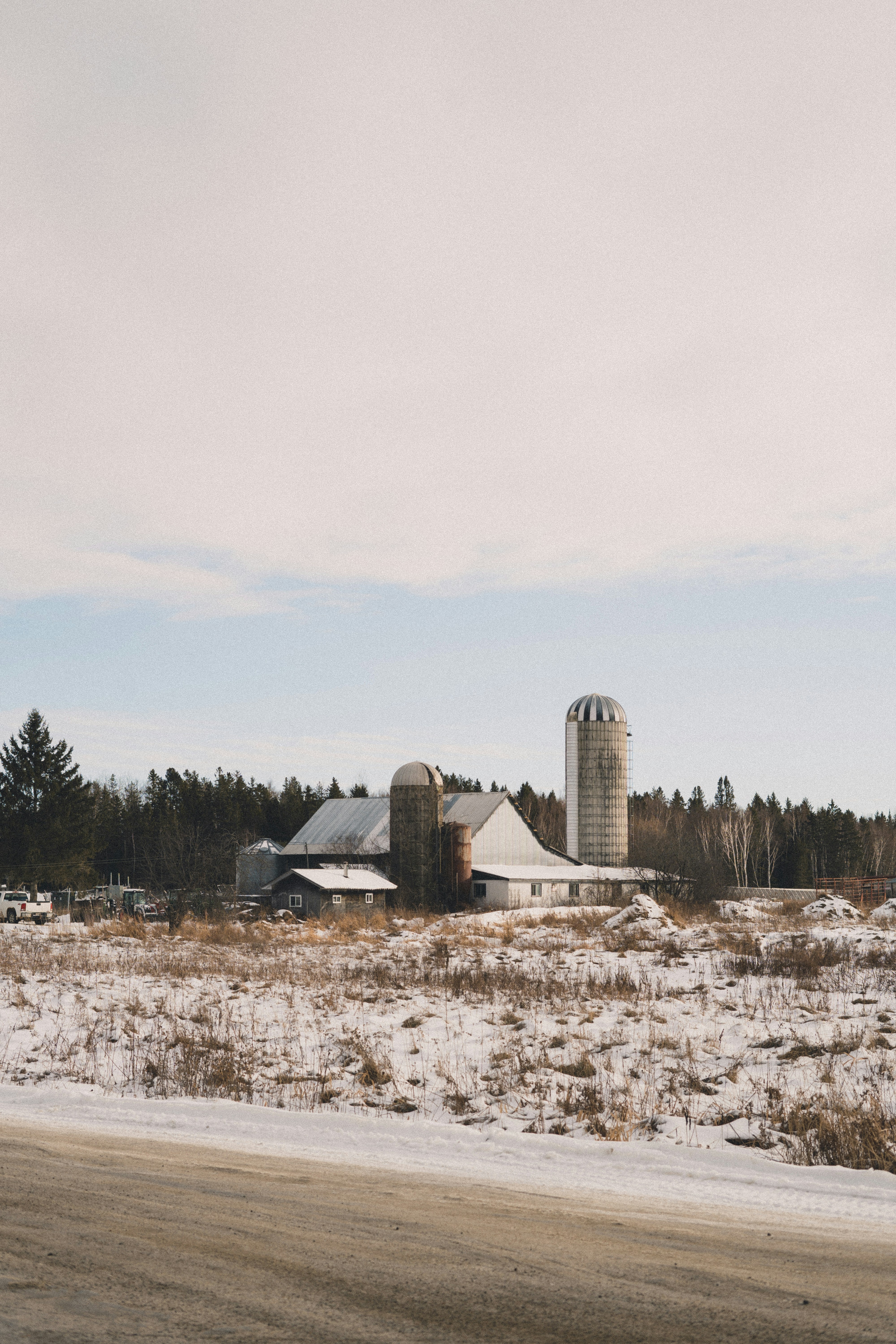 Snow-dusted farm with white barn and silos under a vast winter sky.