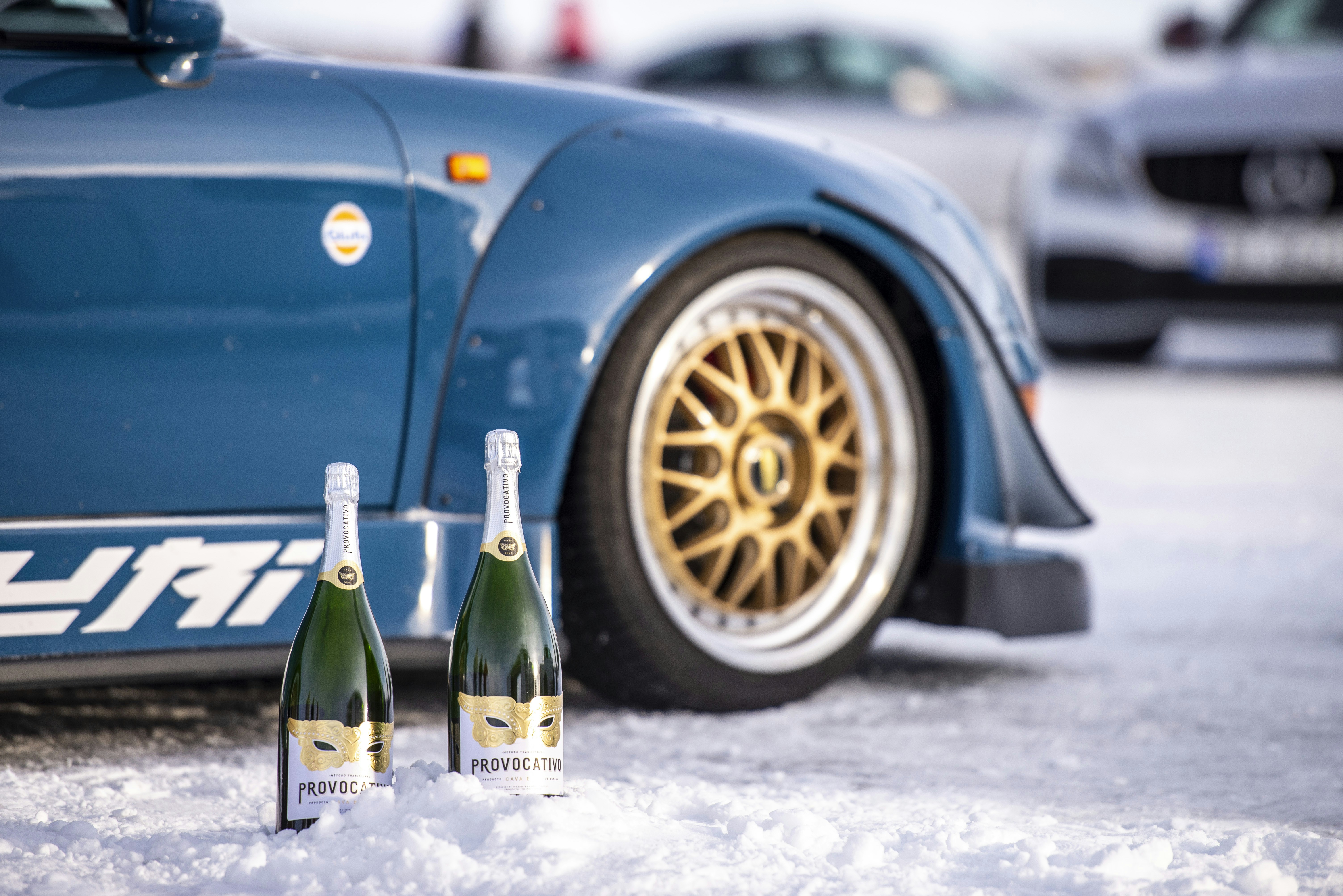 Foto Dos botellas de champán sentadas junto a un auto deportivo azul ...