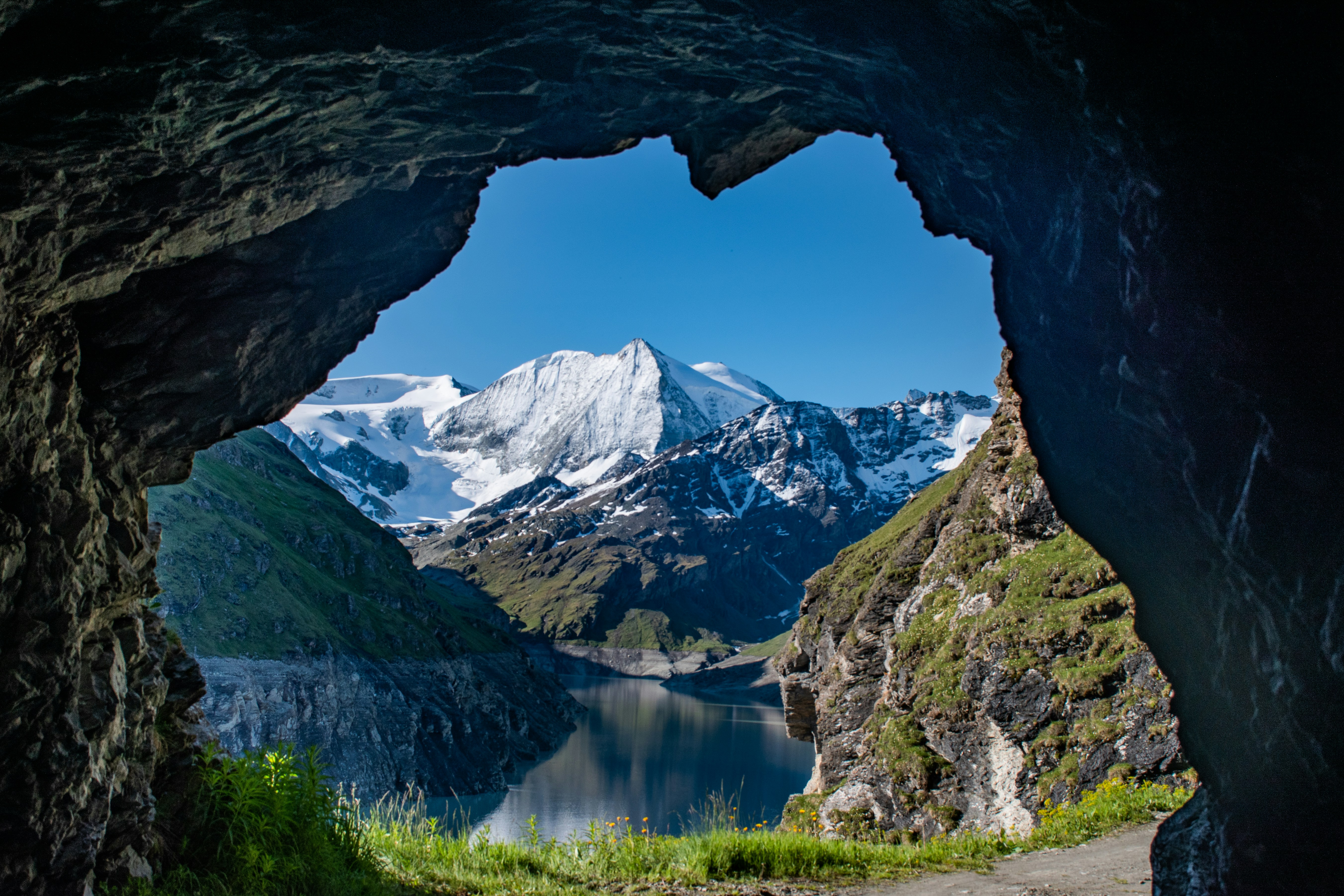 View of snow-capped mountains and a reflective lake through a rocky archway, showcasing the beauty of the alpine landscape.