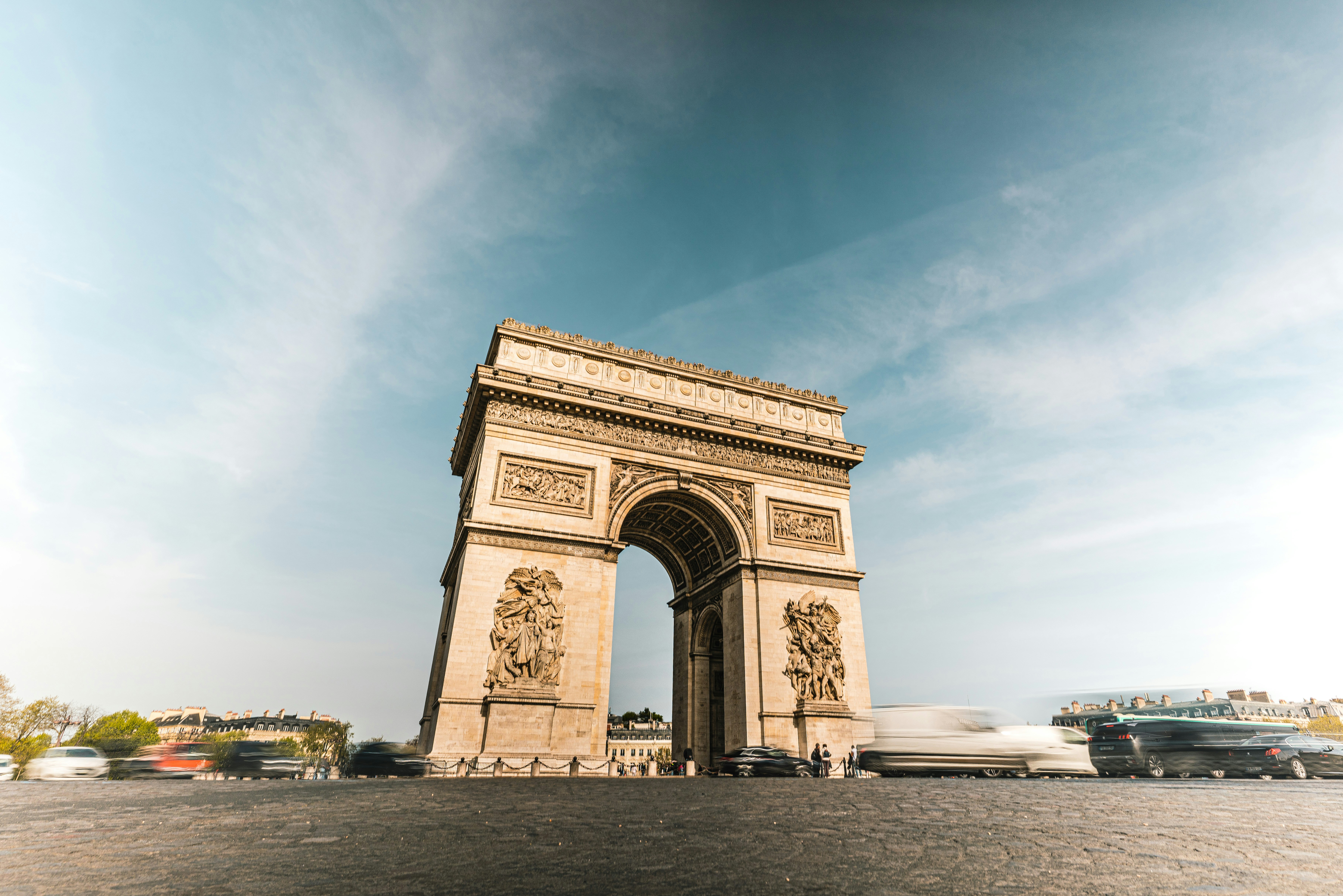 Arc de Triomphe stands majestically against a clear sky, with blurred traffic conveying the dynamic energy of Paris. 
