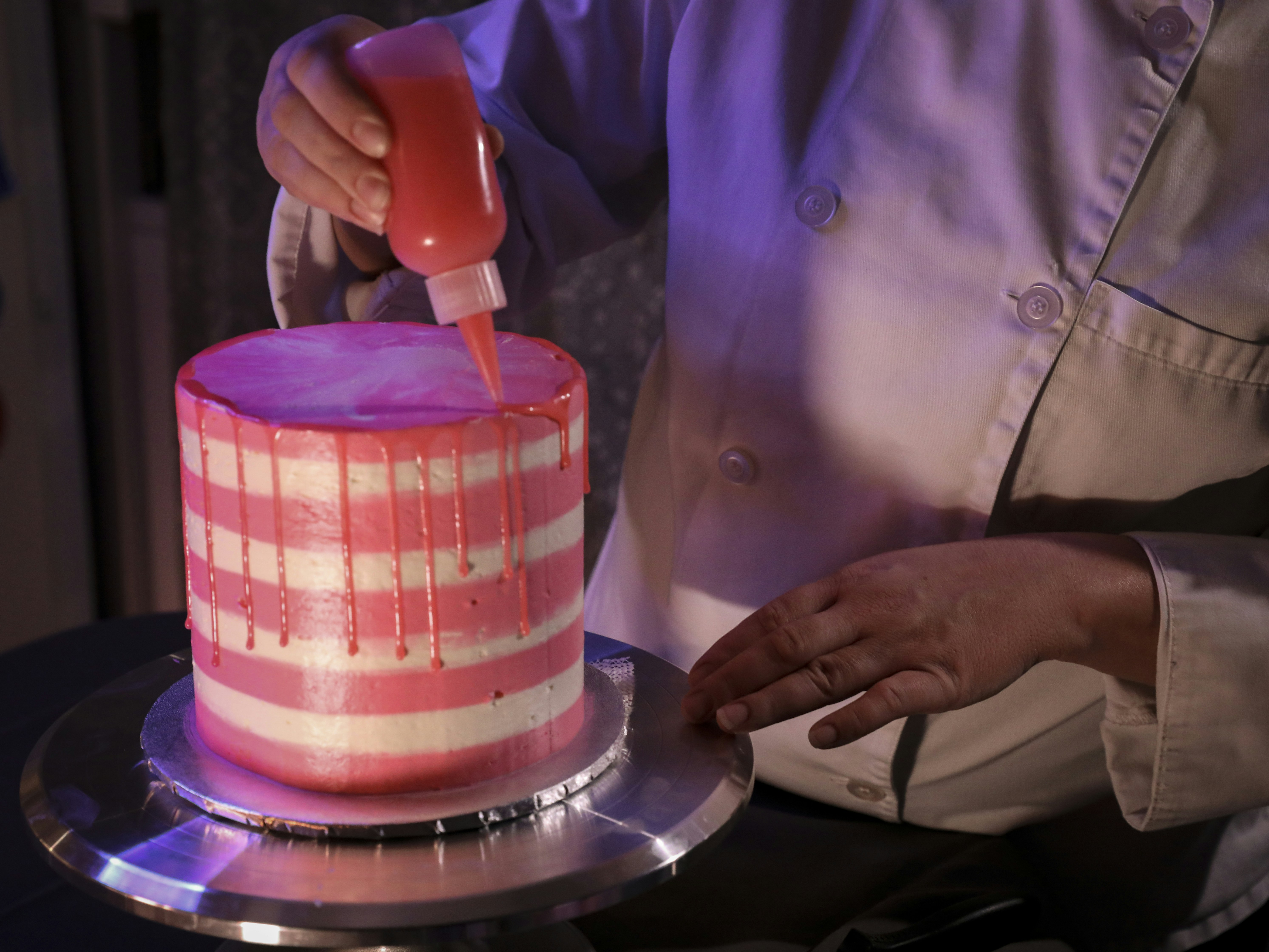 A person is decorating a cake with pink icing photo – Free Baker Image ...