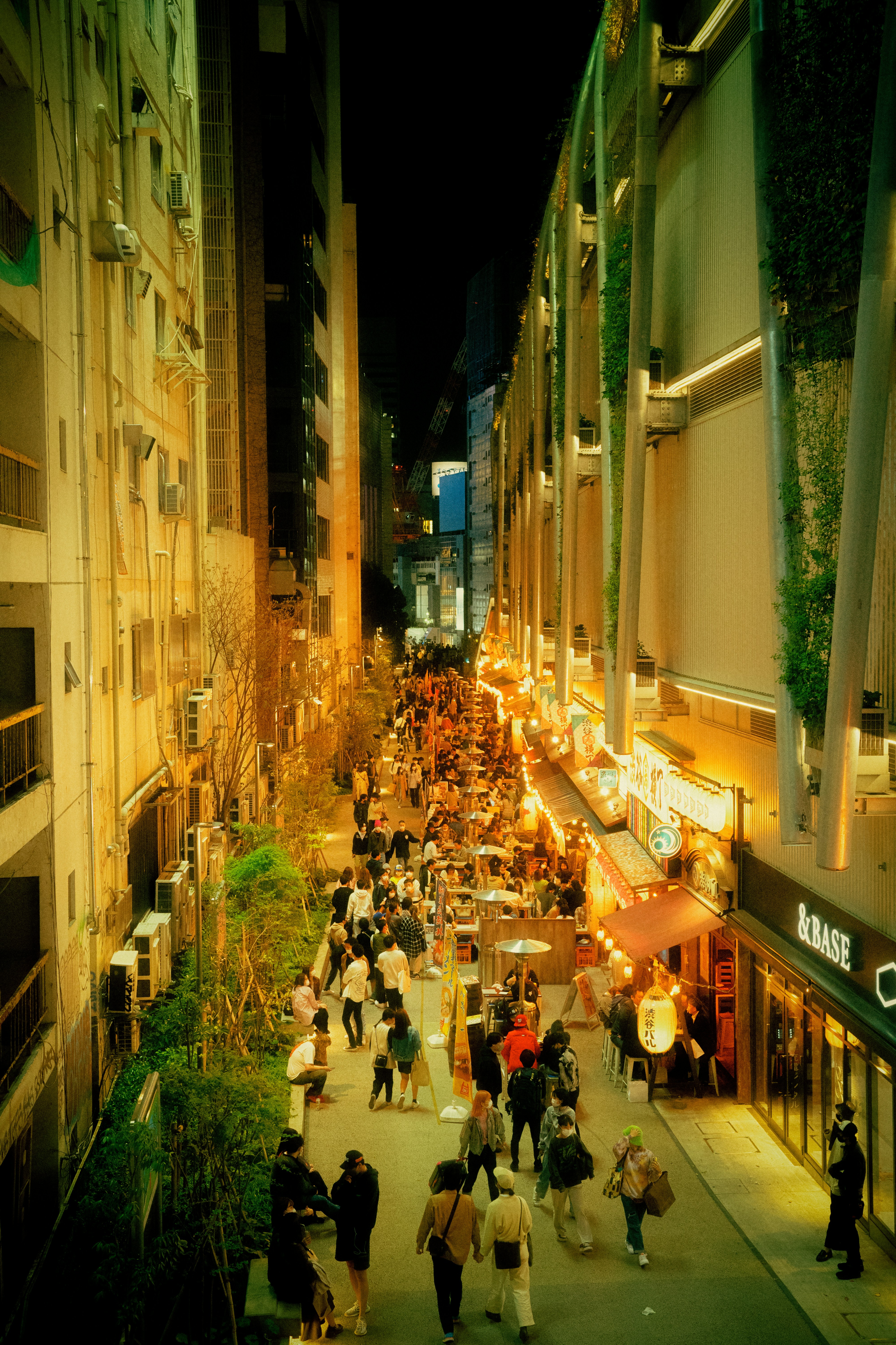 Bustling street filled with diners and vendors under warm lights, showcasing the vibrant nightlife of the city. The scene captures the essence of urban dining culture.