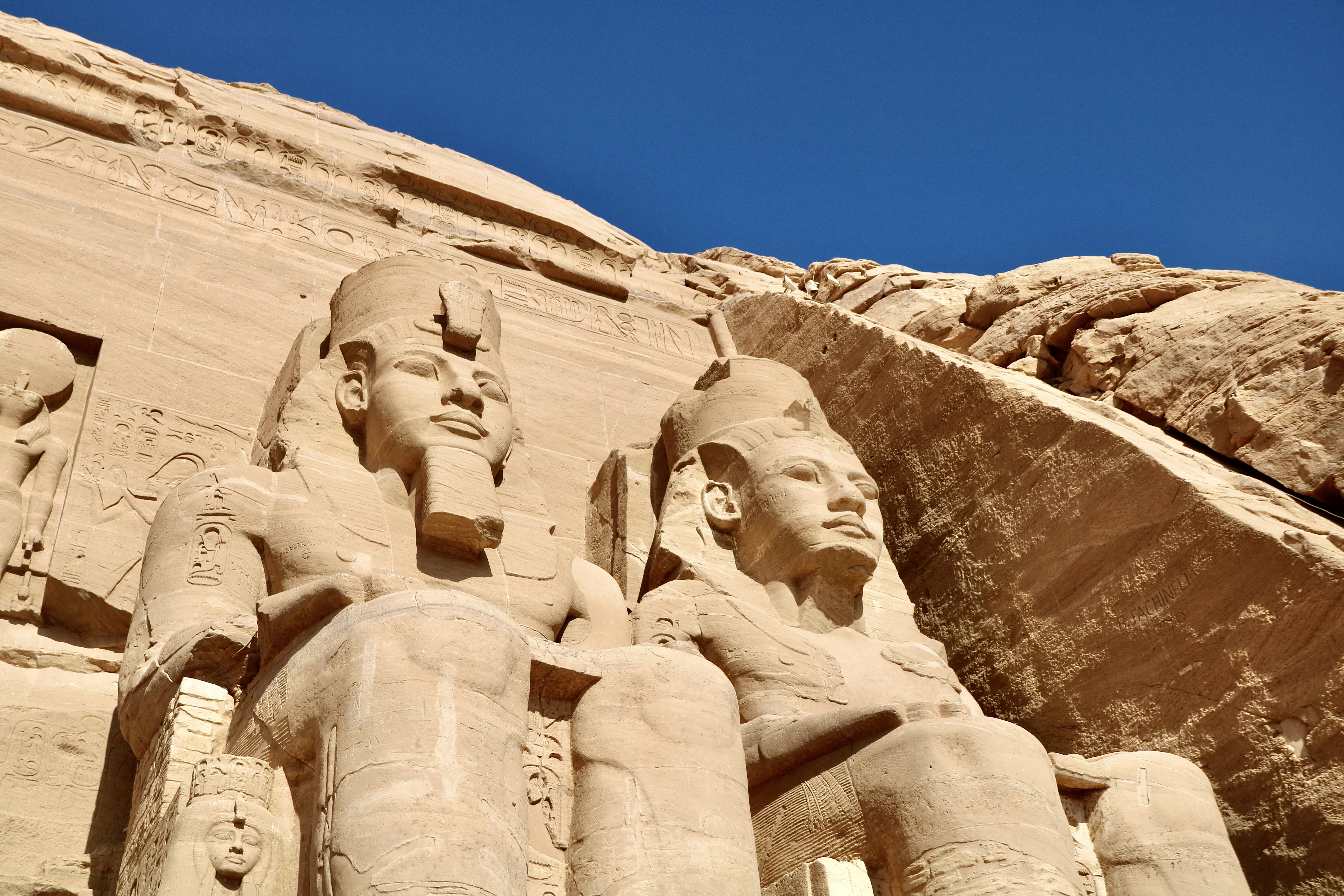 Statues of pharaohs and queens in front of a rock formation photo ...