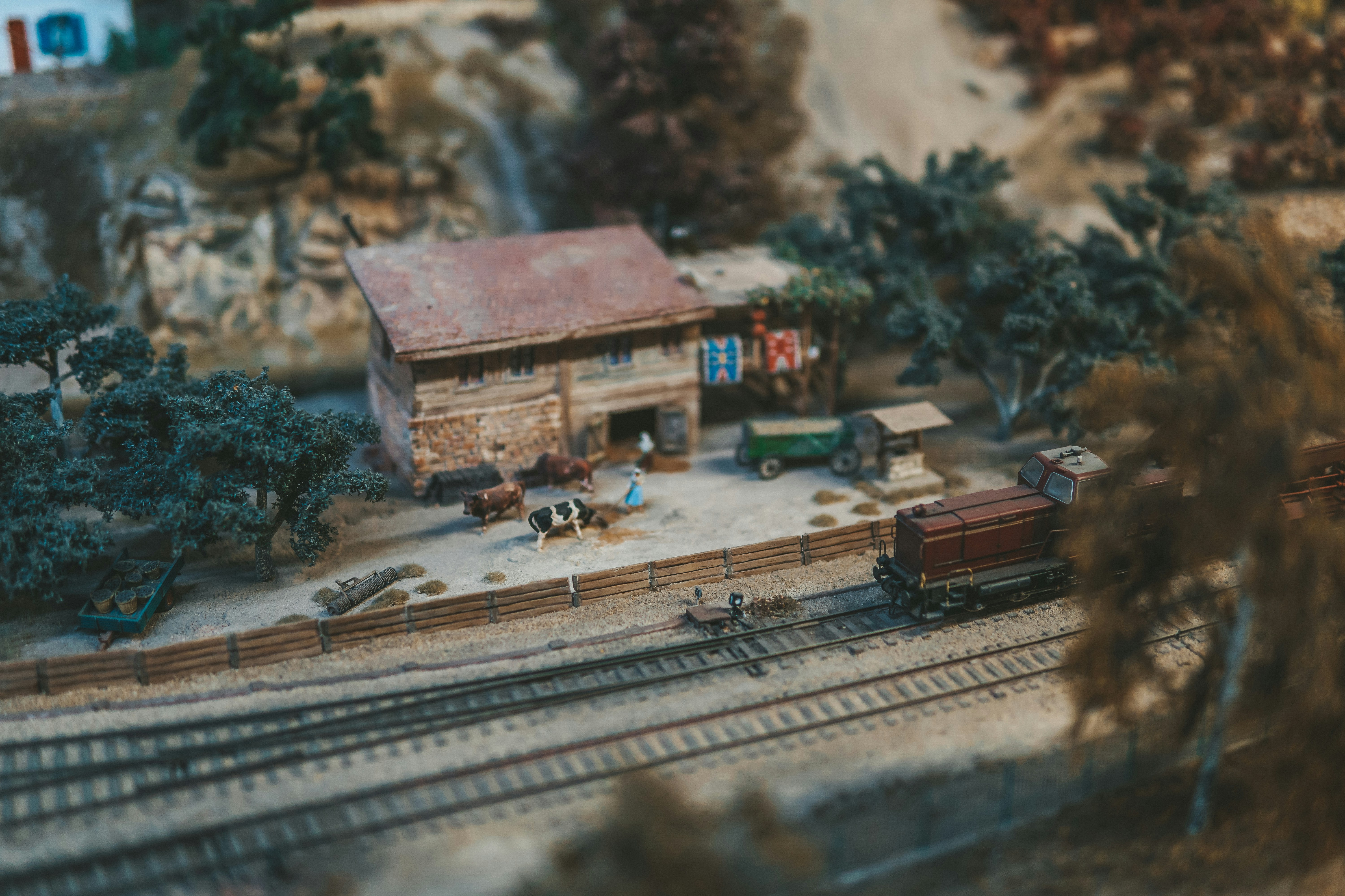 A detailed model scene featuring a rustic farmhouse, a cow, and a train on nearby tracks, showcasing the charm of miniature landscapes.