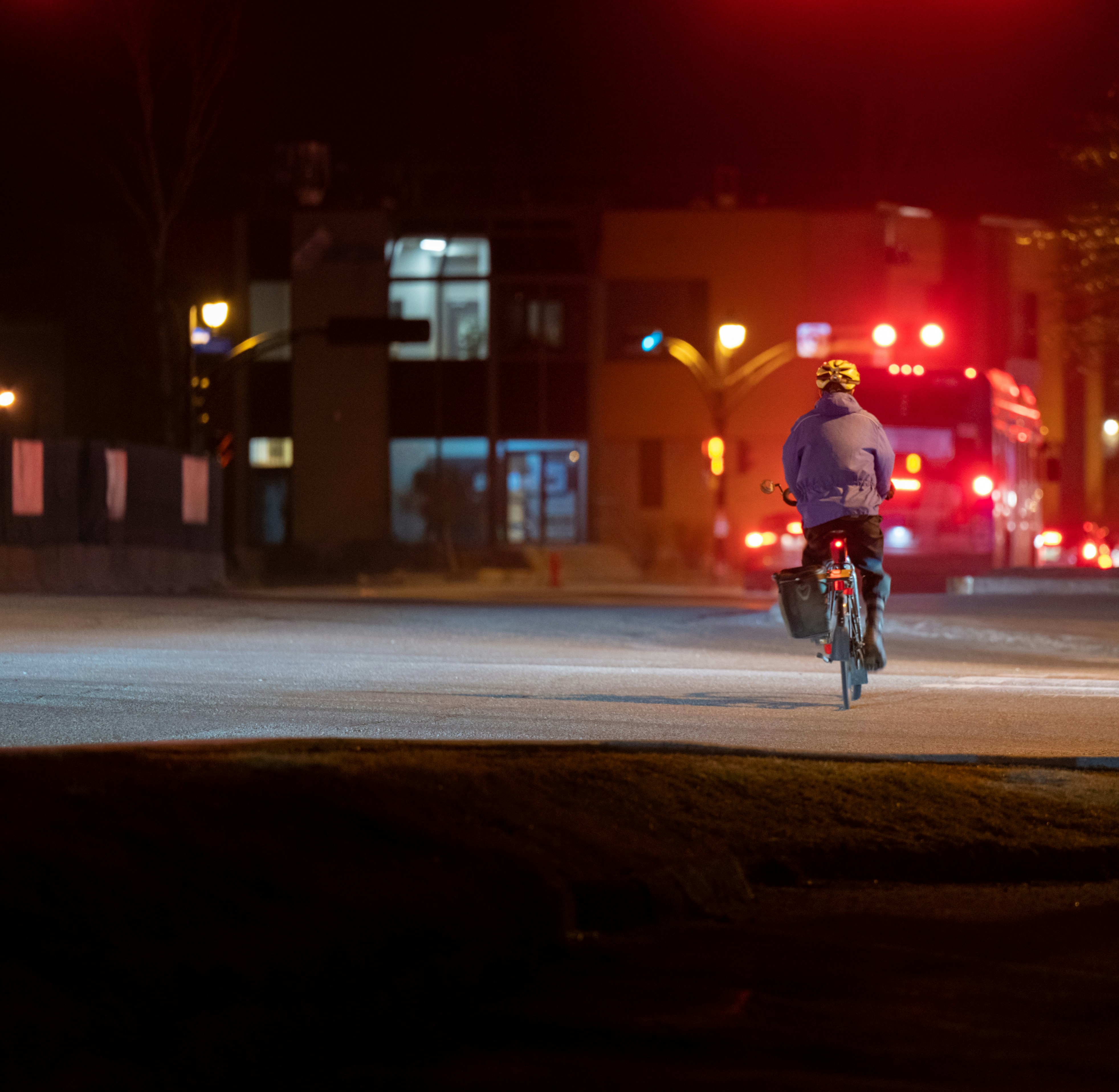 Cyclist navigating a city street illuminated by traffic lights and nearby buildings at night.