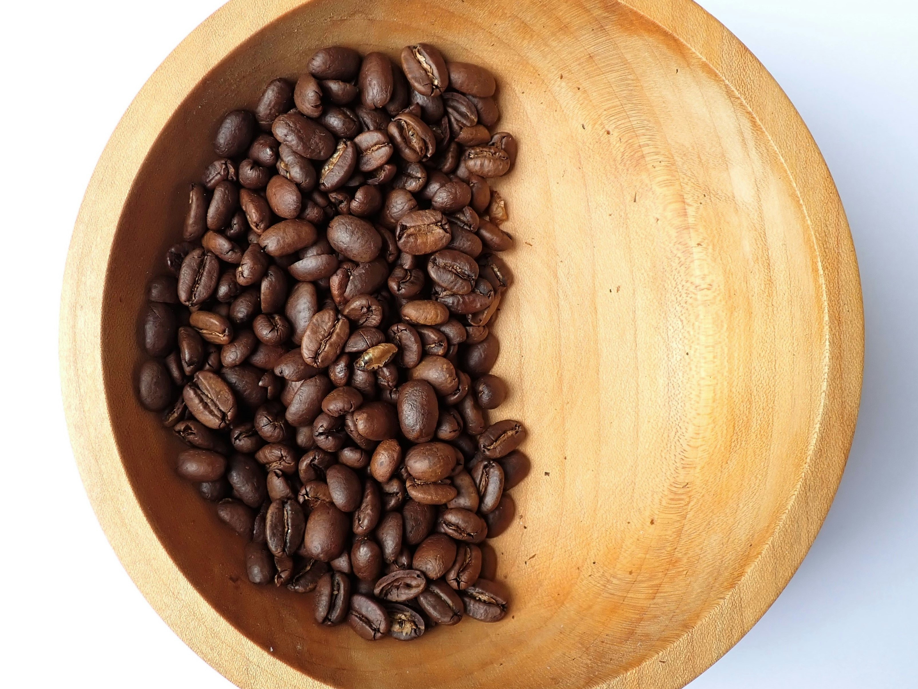 A wooden bowl filled with an assortment of roasted coffee beans, showcasing their rich, dark hues and varied textures.