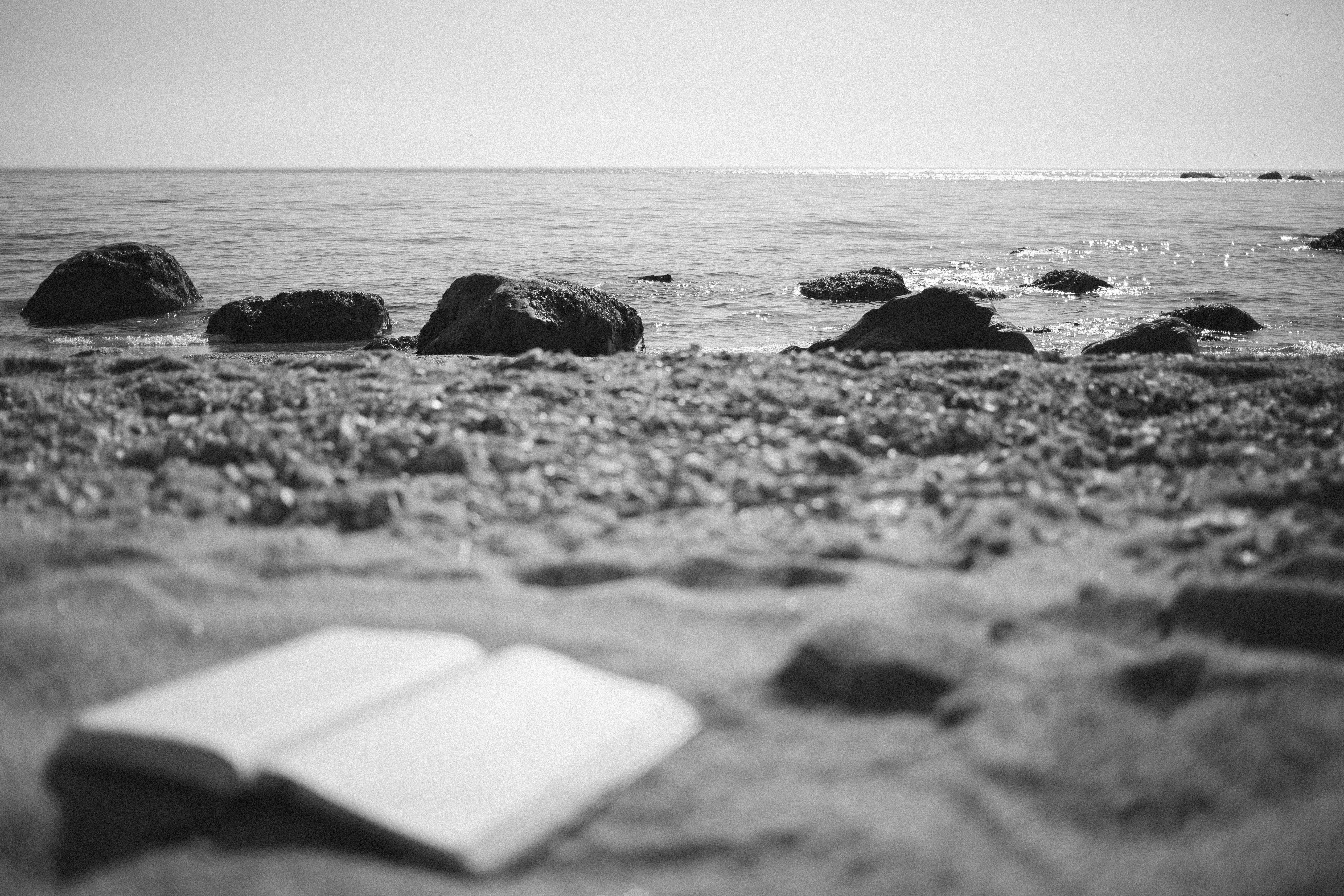 Monochrome Shoreline: Open Book on Pebbles Beneath a Quiet Sea