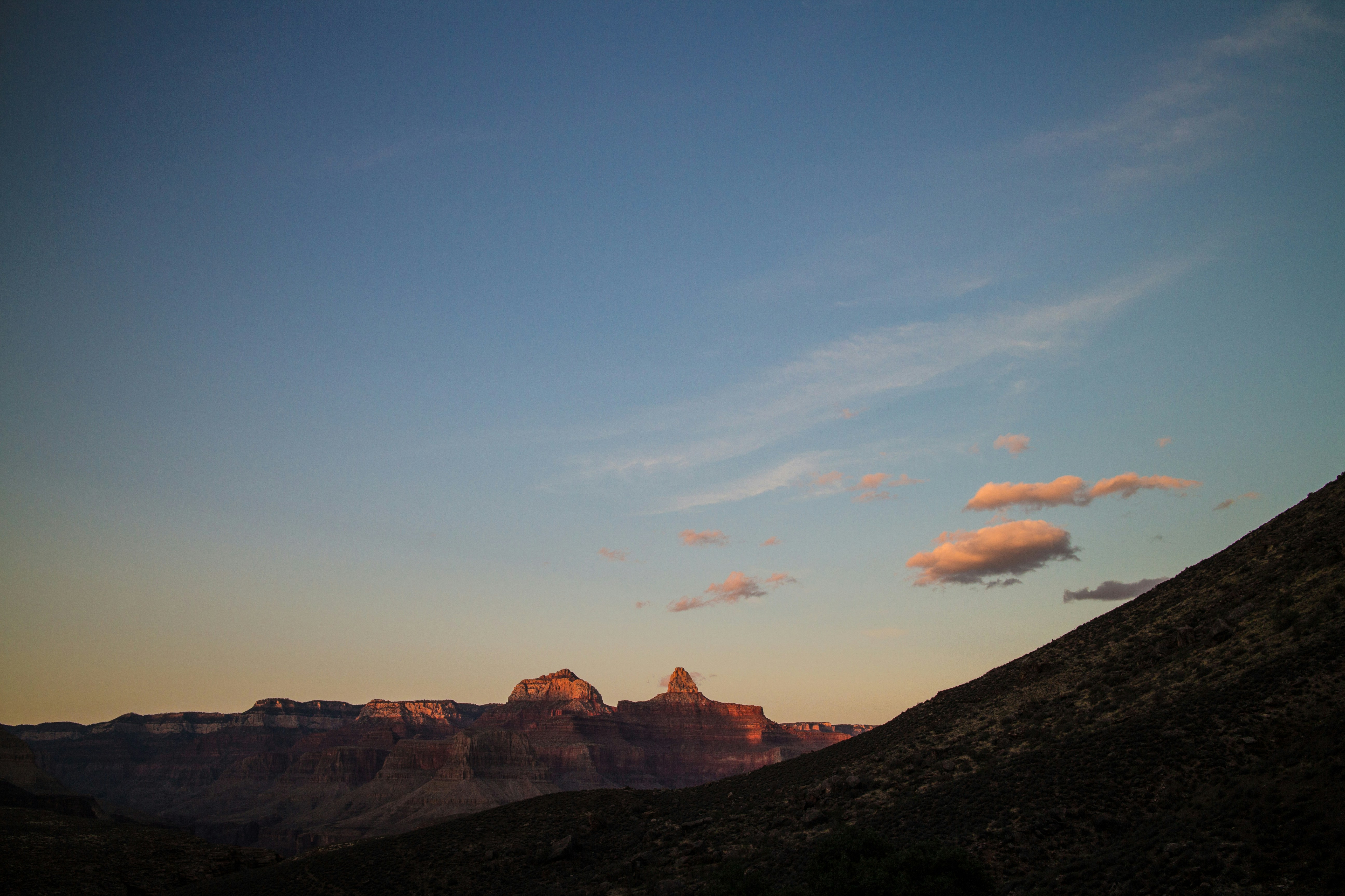 A serene landscape featuring the majestic peaks of the Grand Canyon under a twilight sky, with soft clouds drifting above. The warm hues of sunset illuminate the rocky formations.