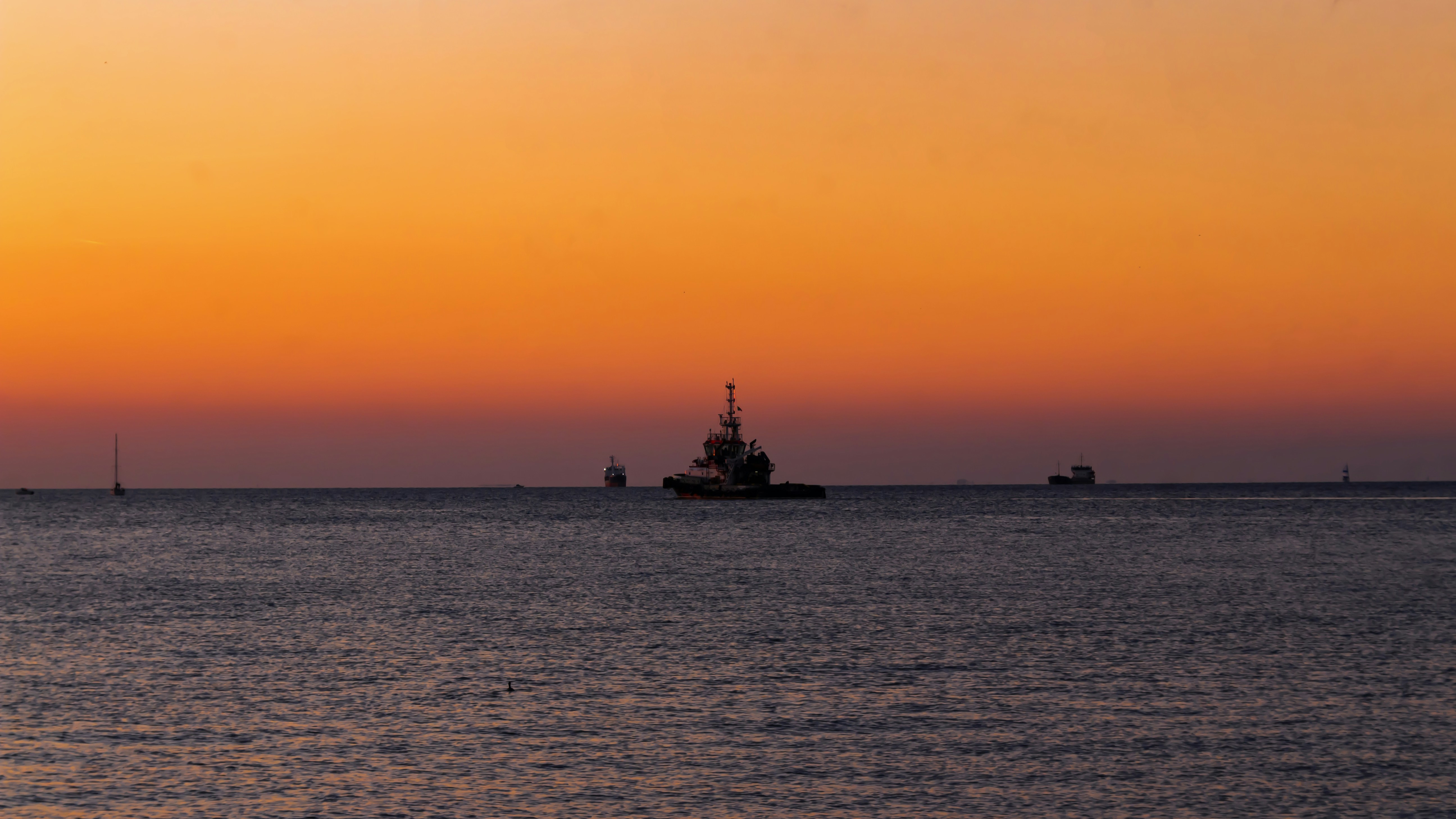 Silhouetted boat against a vibrant orange sunset over calm ocean waters.