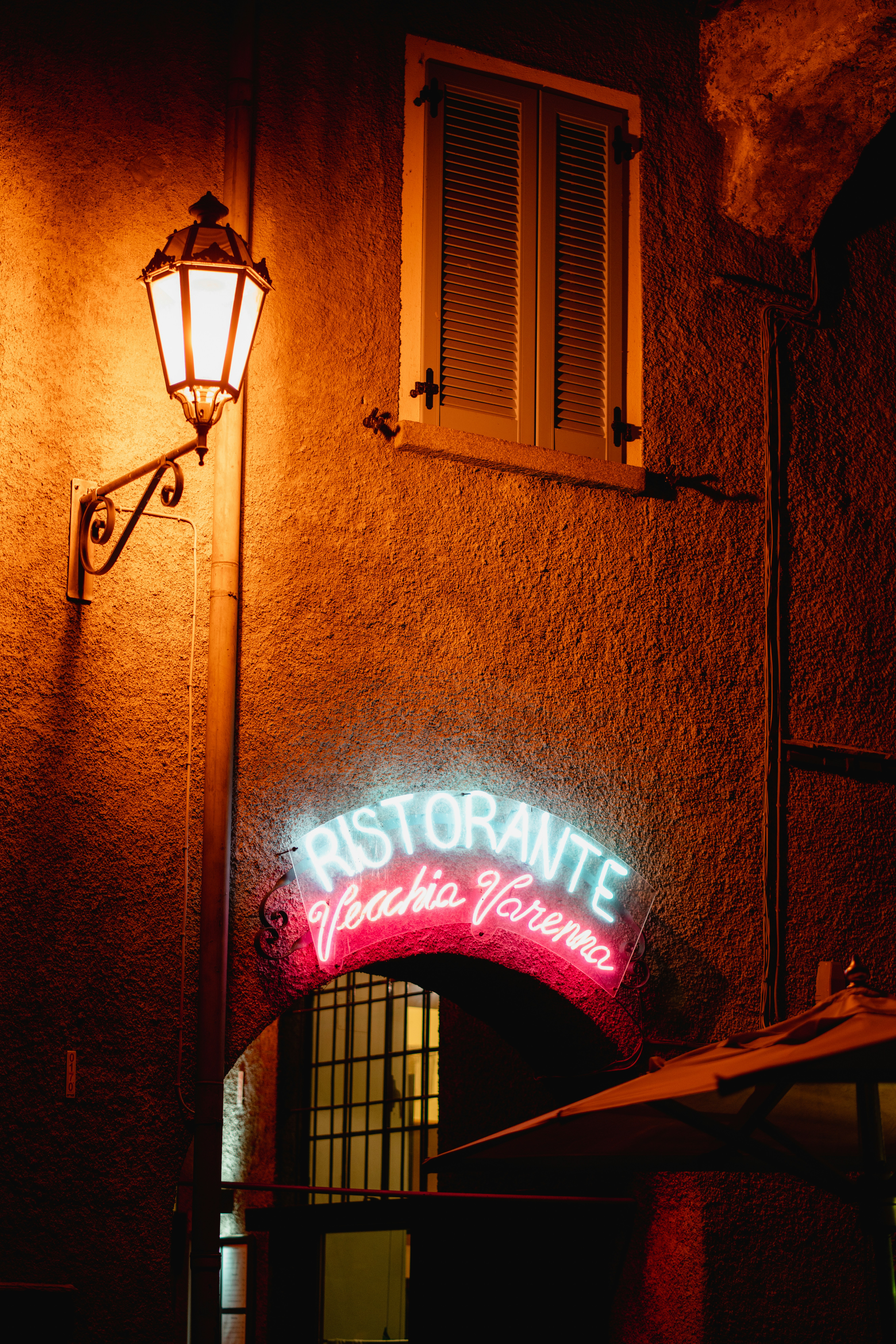 Night scene on a textured stucco wall with a warm streetlamp and a neon Ristorante sign above a doorway.