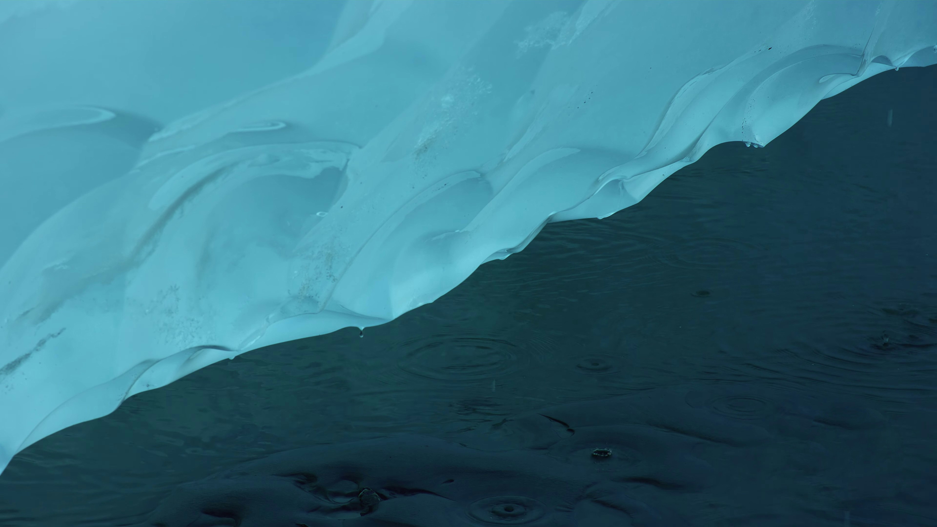 Curved edge of a glacier meets dark, rippling water, highlighting the contrast between ice and liquid. The scene captures the tranquil yet dynamic relationship of nature.