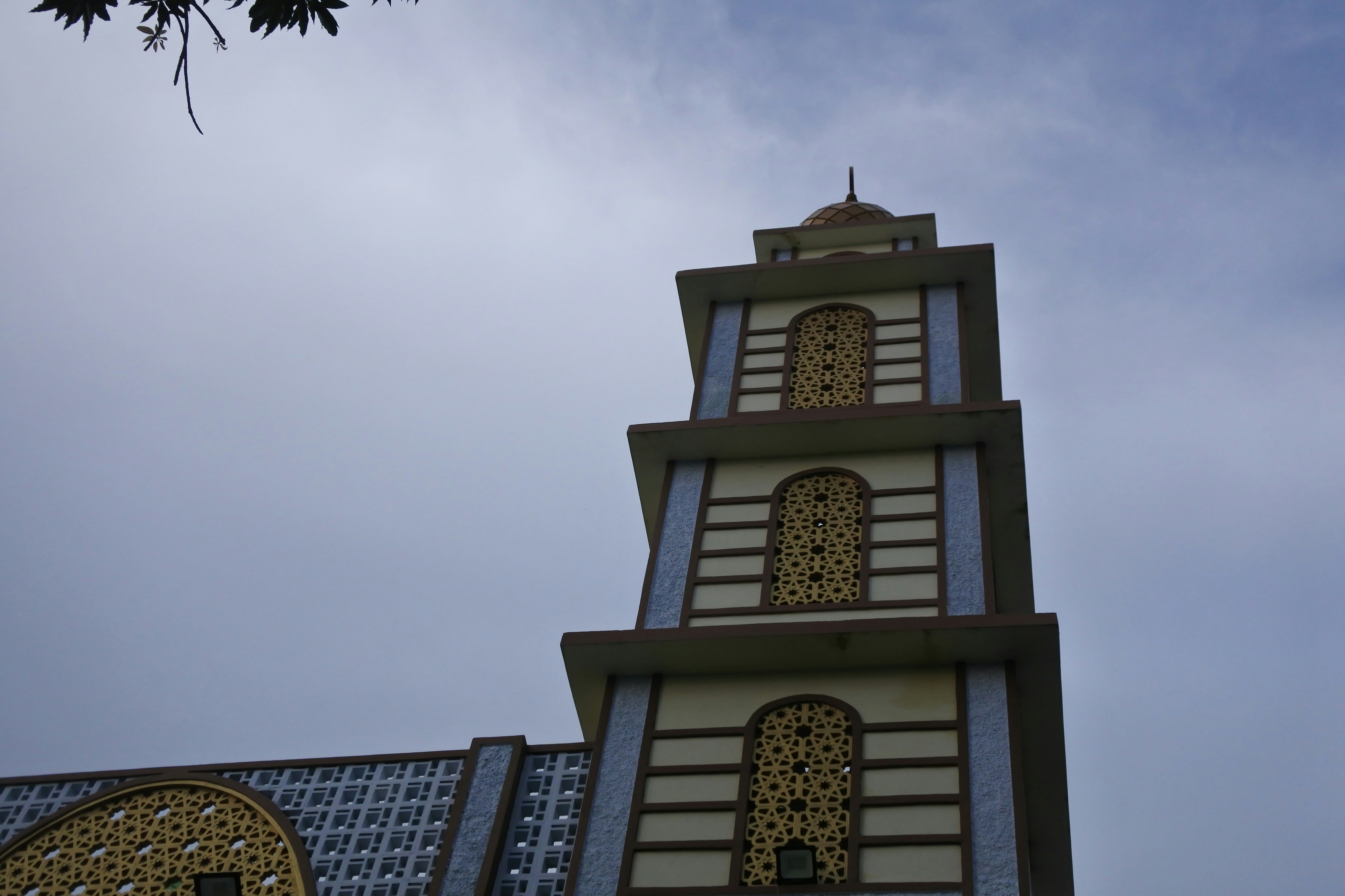Tall architectural structure with intricate patterns and a domed top against a cloudy sky.