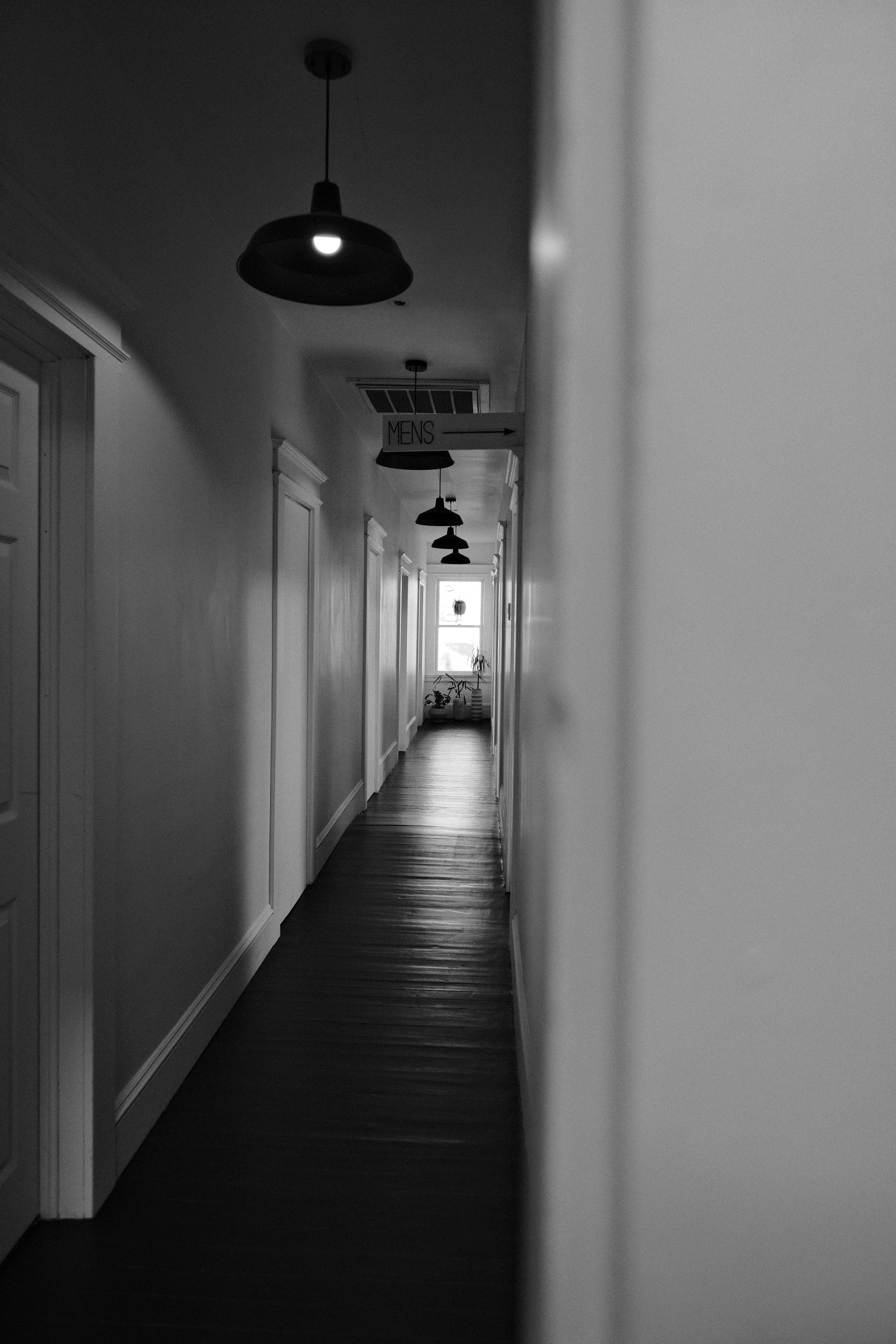 Narrow hallway illuminated by pendant lights, leading to a window at the far end, creating a sense of depth and perspective.