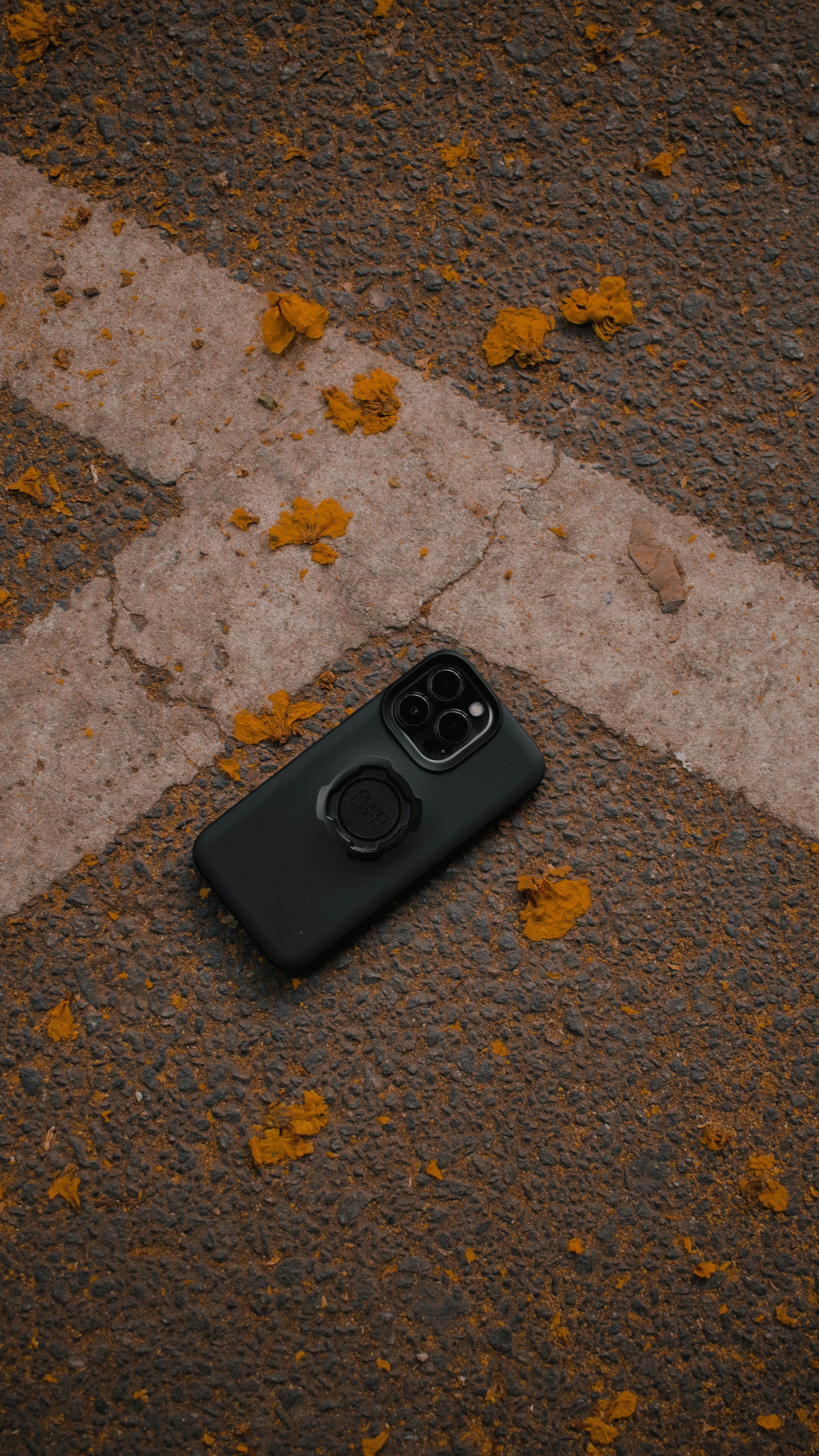 A black smartphone rests on a textured surface, surrounded by scattered orange petals, highlighting a moment of urban tranquility.