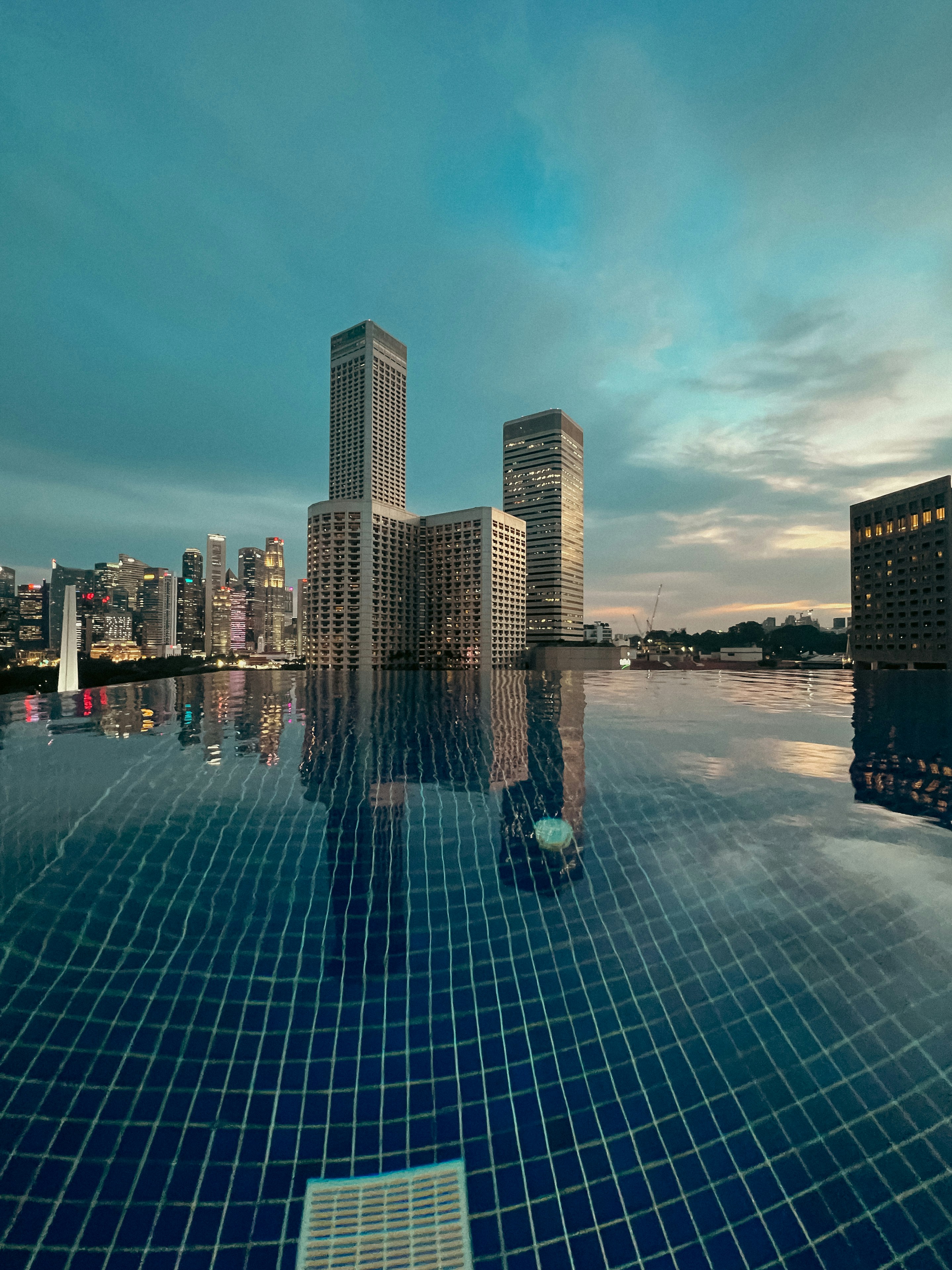 Infinity pool reflecting the skyline of a bustling city at dusk, with modern architecture and a serene atmosphere.