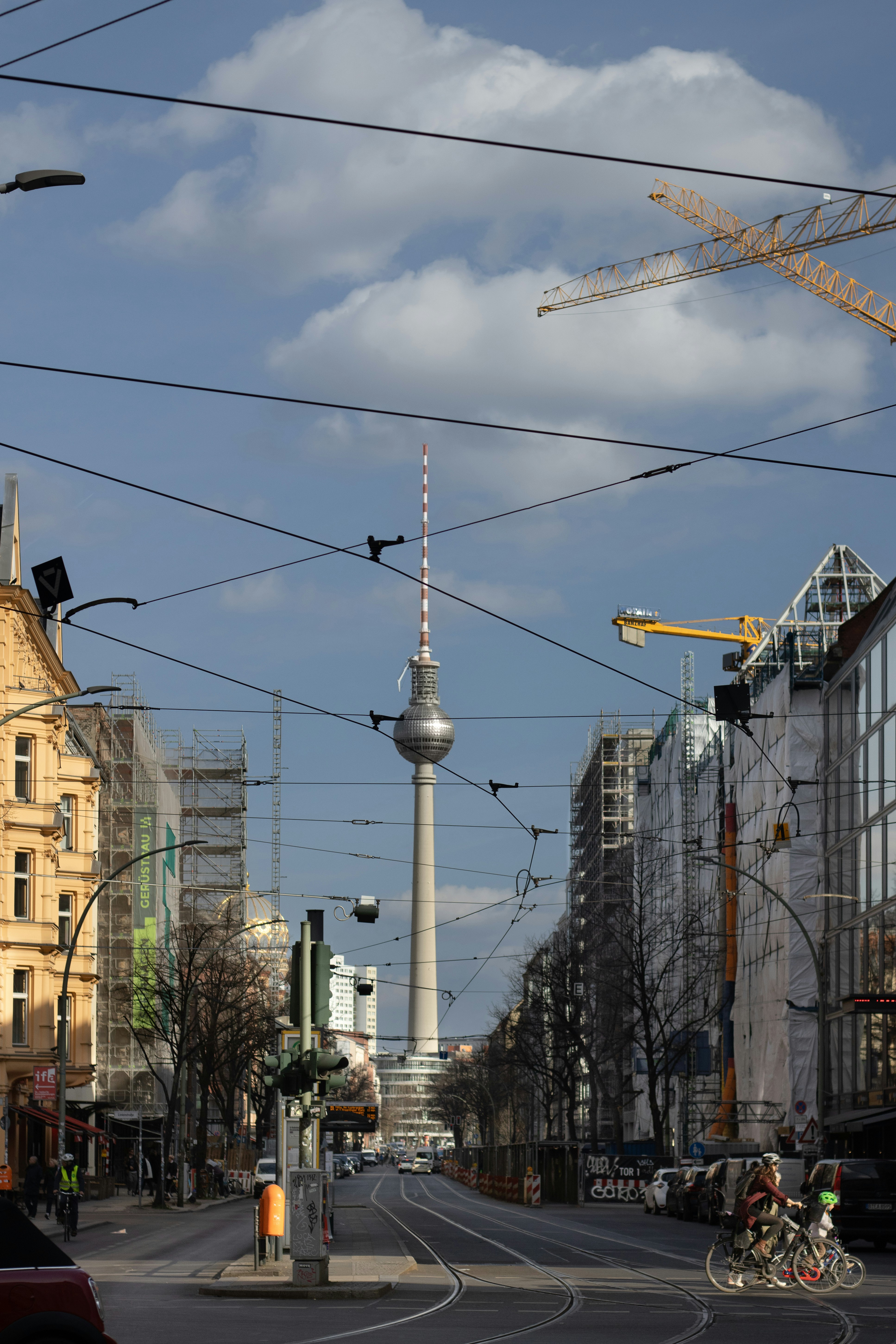 Berlin's iconic TV Tower rises above a bustling street scene, framed by construction and urban life. A blend of historic and modern architecture creates a dynamic cityscape.