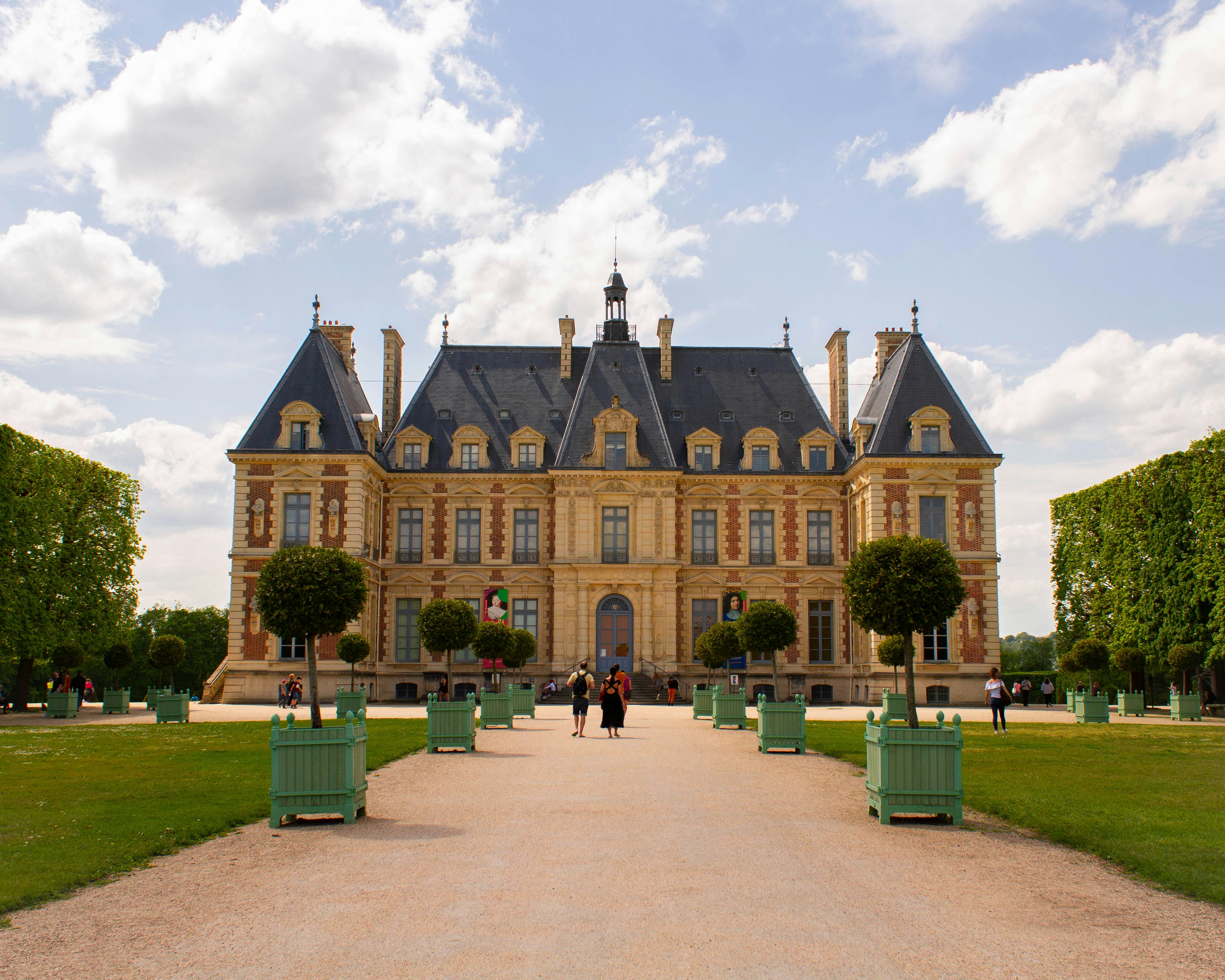 Elegant chateau surrounded by manicured gardens and visitors, showcasing classical architecture and vibrant greenery.