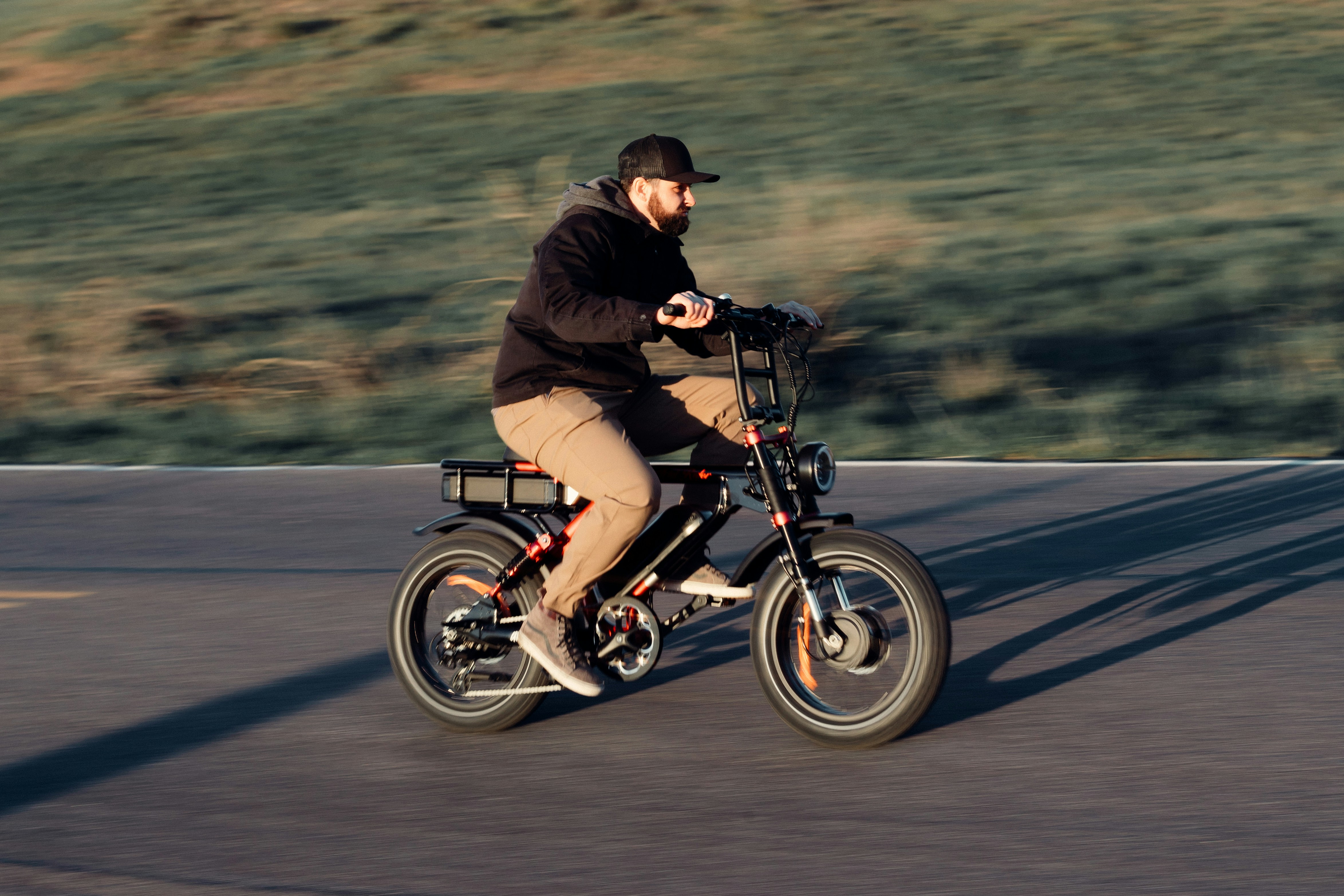 A man rides an electric bike on a smooth road, showcasing motion and speed against a blurred green backdrop.
