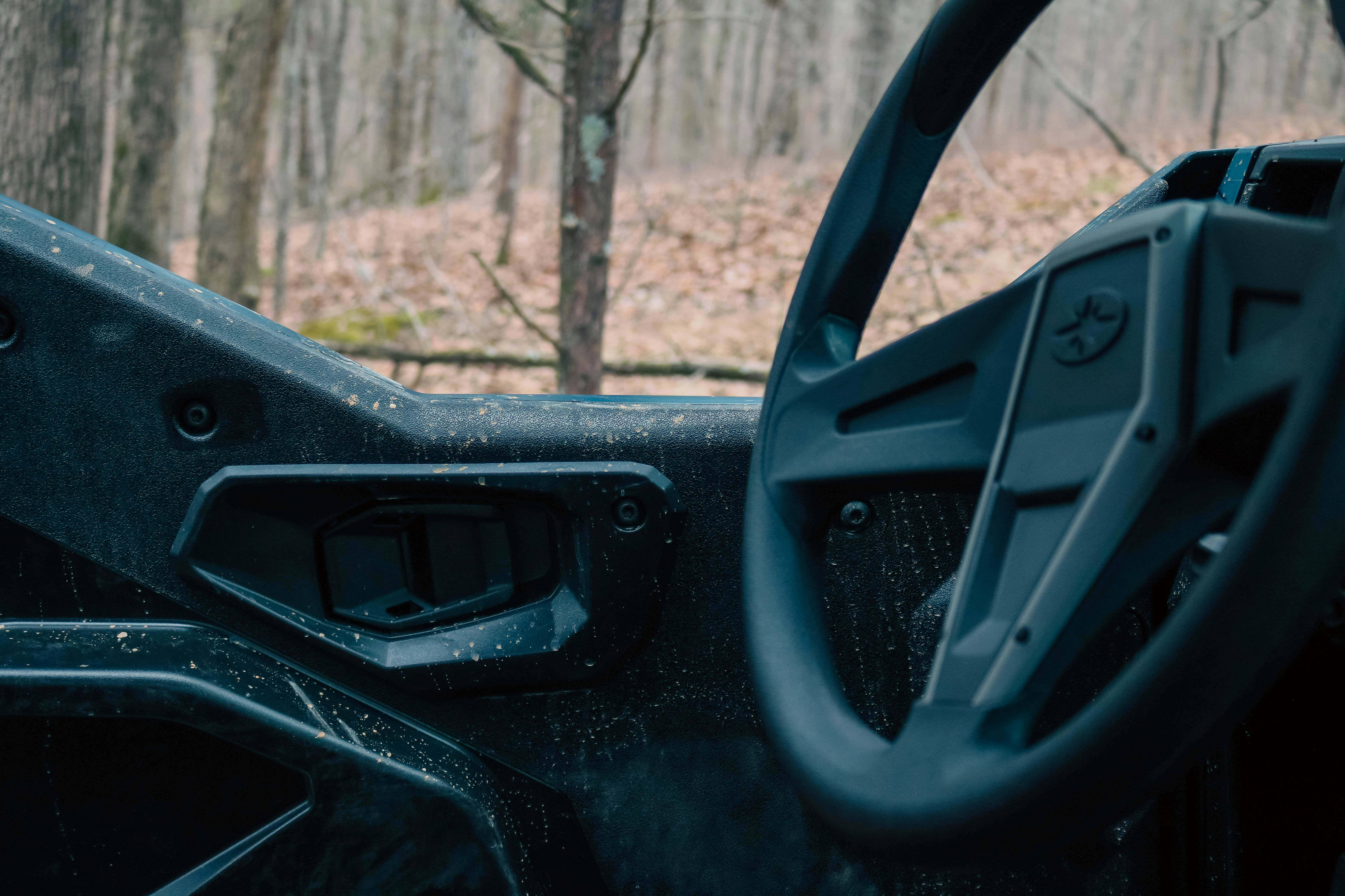 Interior view of an off-road vehicle showcasing the steering wheel and control panel, set against a backdrop of a tranquil forest.