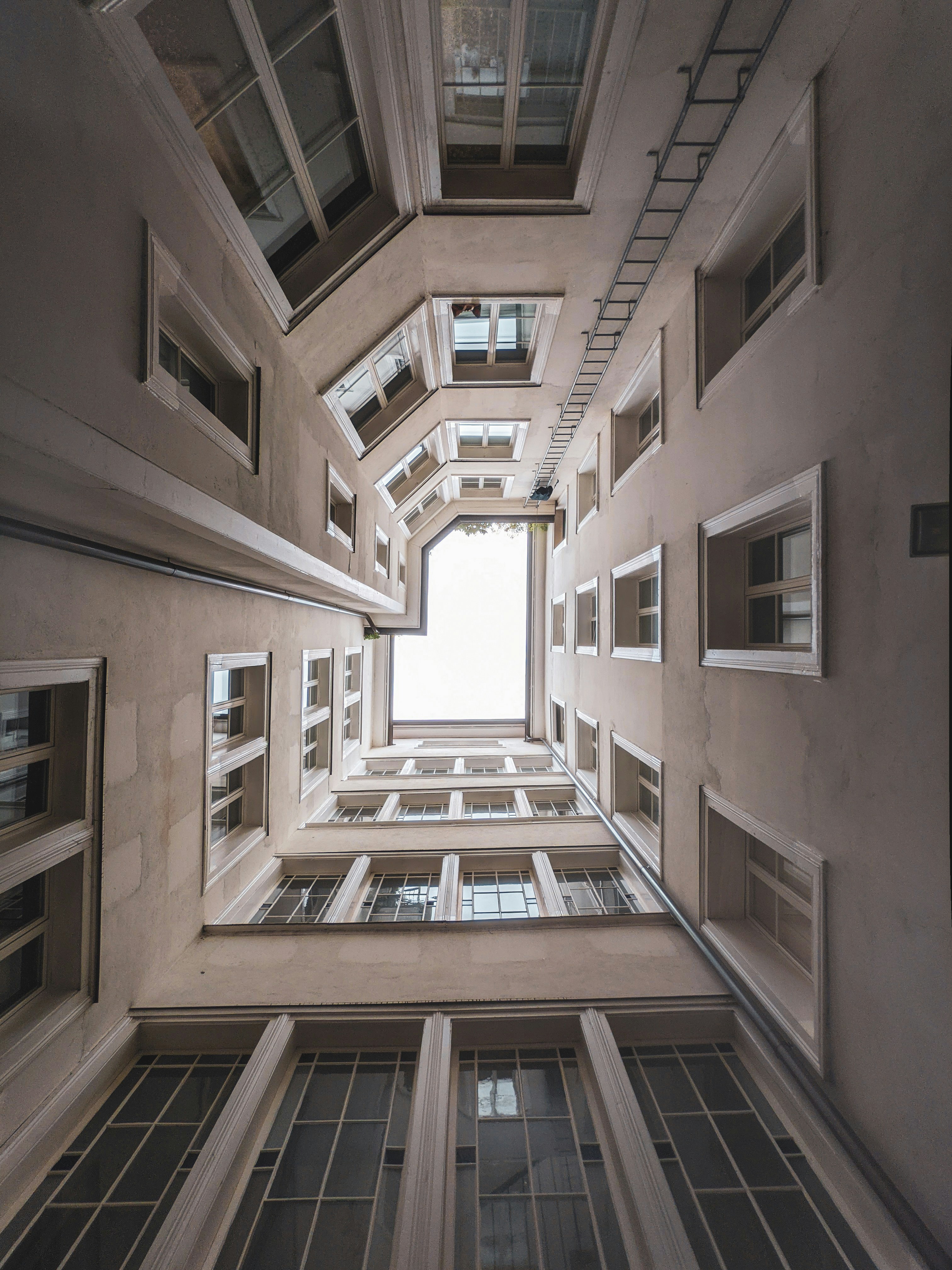 Looking up through a geometric courtyard, showcasing a harmonious arrangement of windows and walls converging towards the sky.