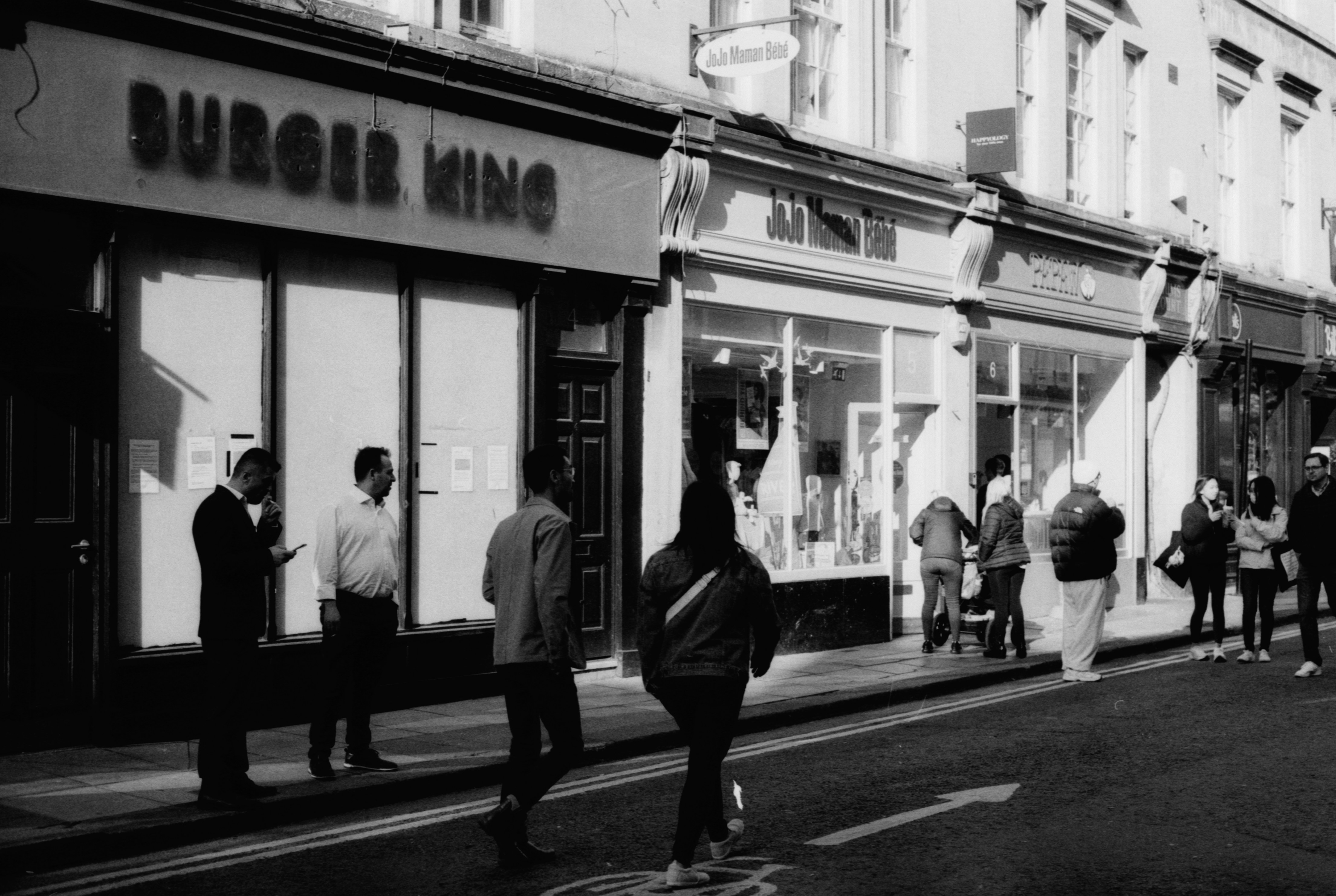 Monochrome Crossing: Pedestrians Align with Shopfronts Beneath Signage