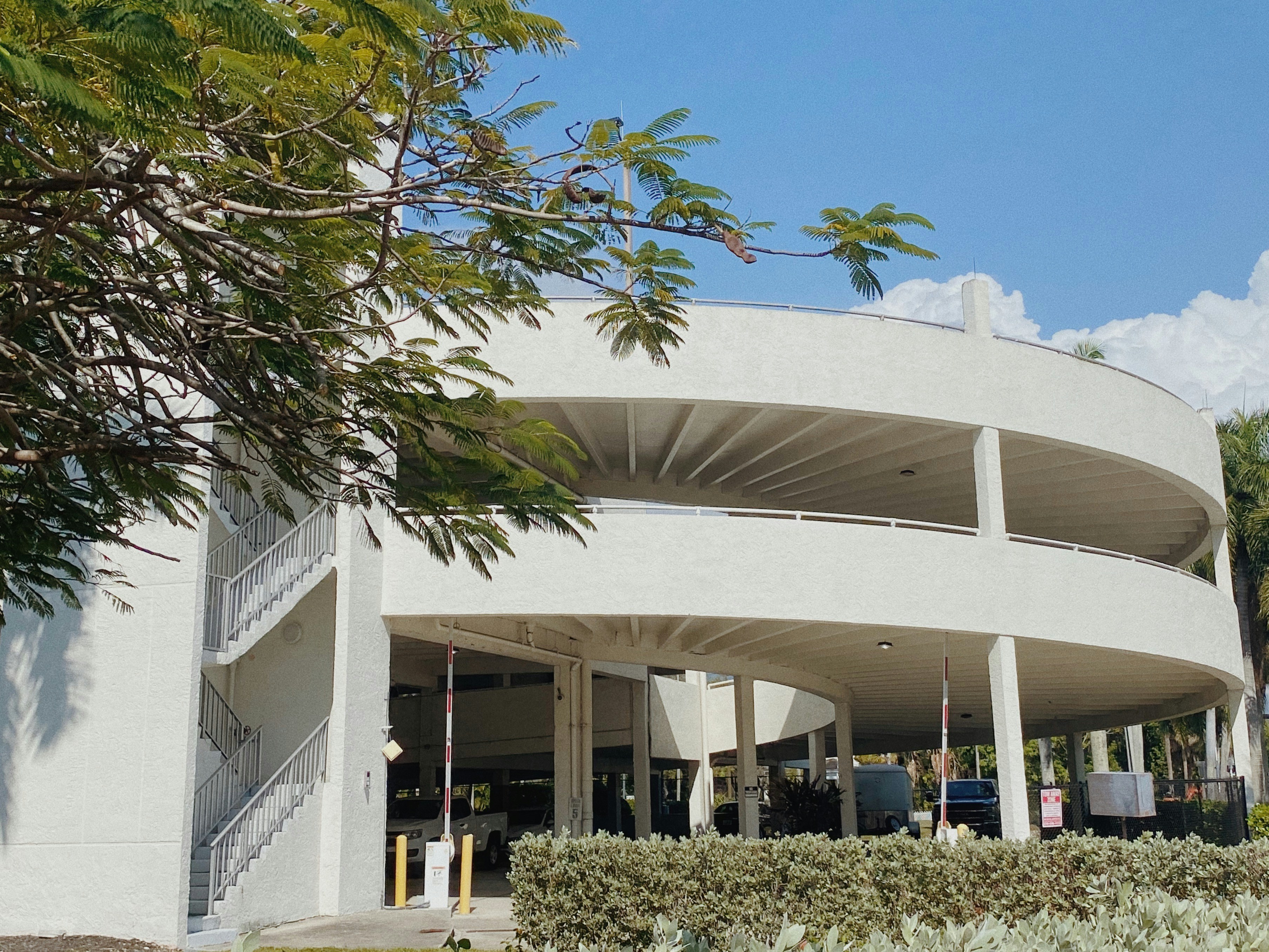 Modern white building with a spiral ramp design, set against a backdrop of lush greenery under a clear blue sky.