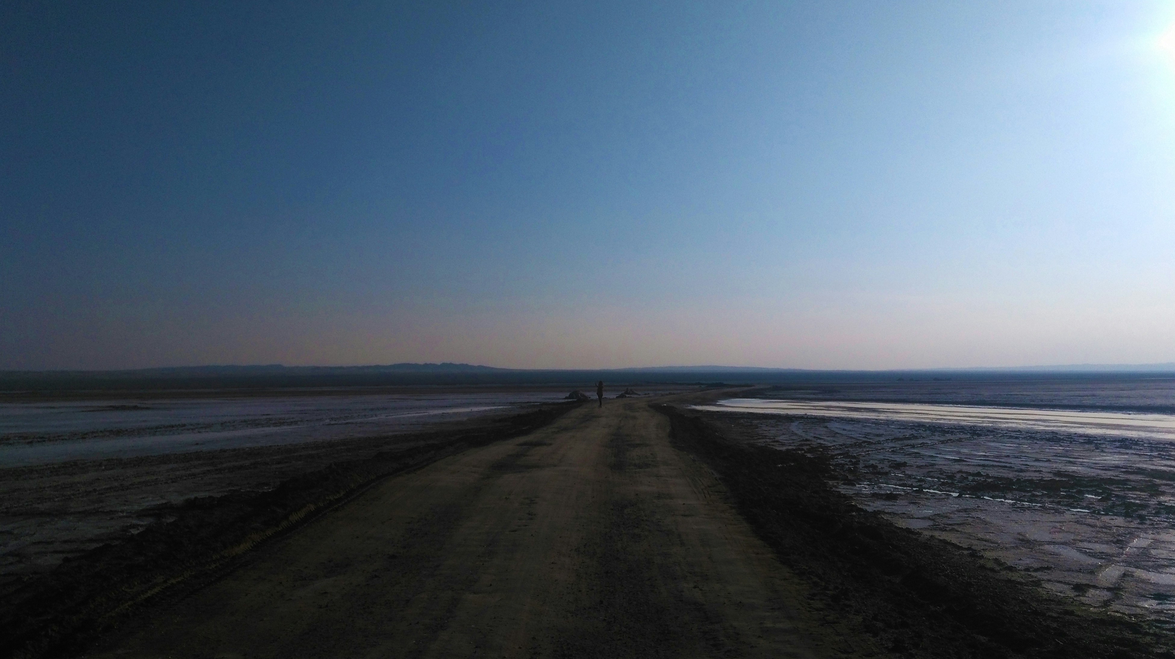 Dirt road stretches into a vast desert landscape under a clear blue sky.