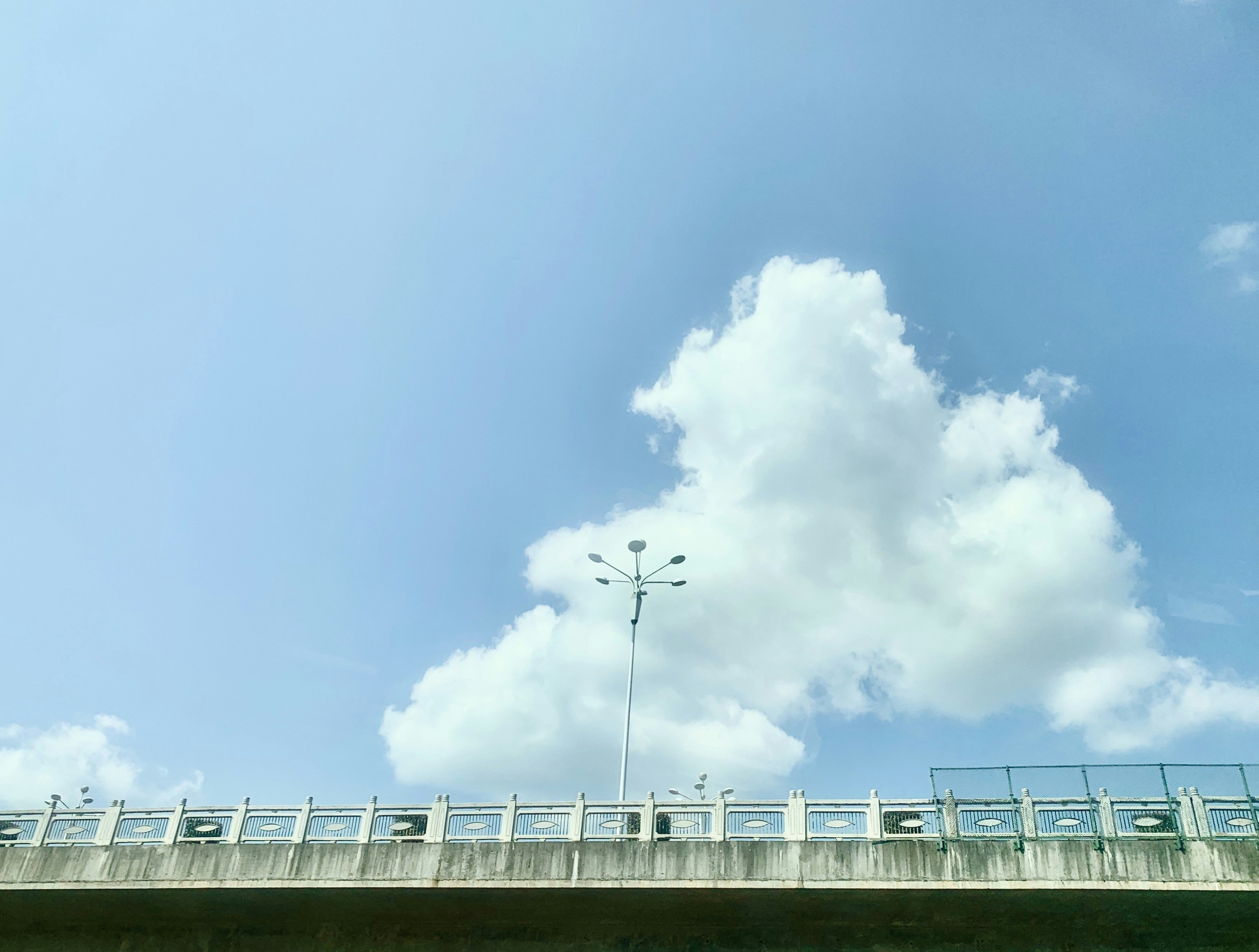 A bridge with a streetlamp under a vast blue sky dotted with fluffy clouds.