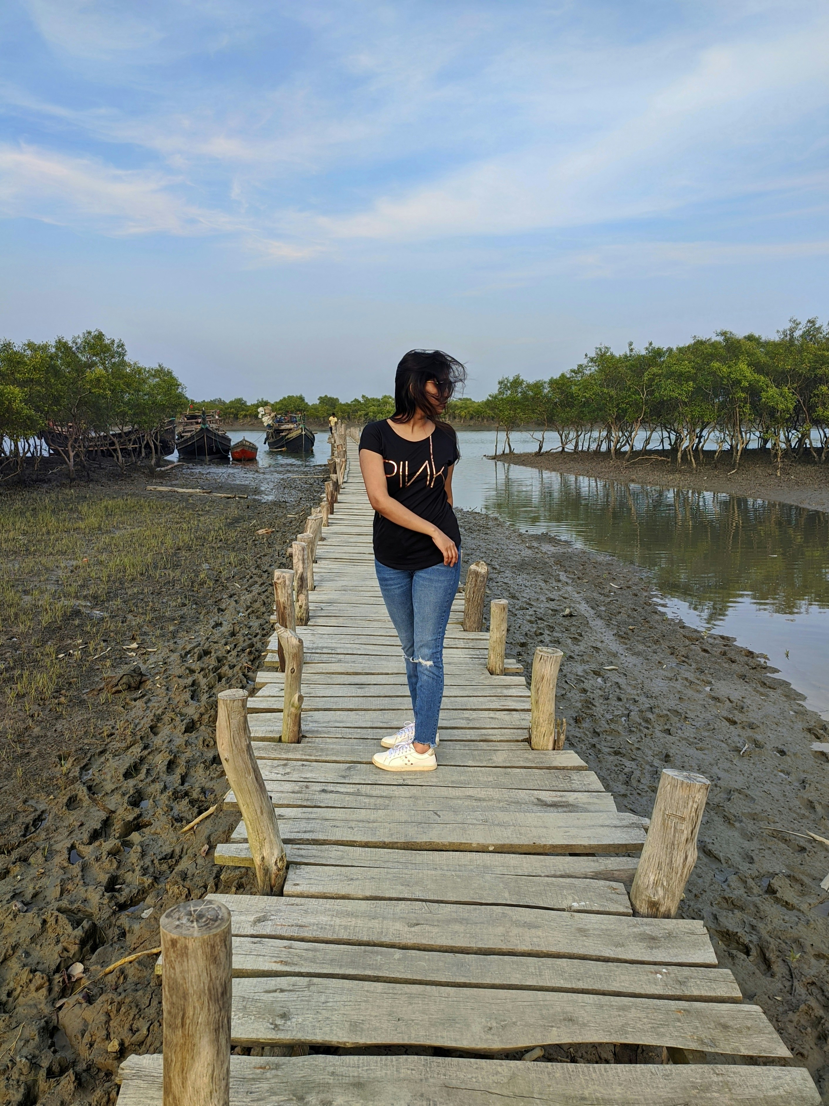 Woman in black tee on a weathered wooden boardwalk stretching through mangrove pools at low tide