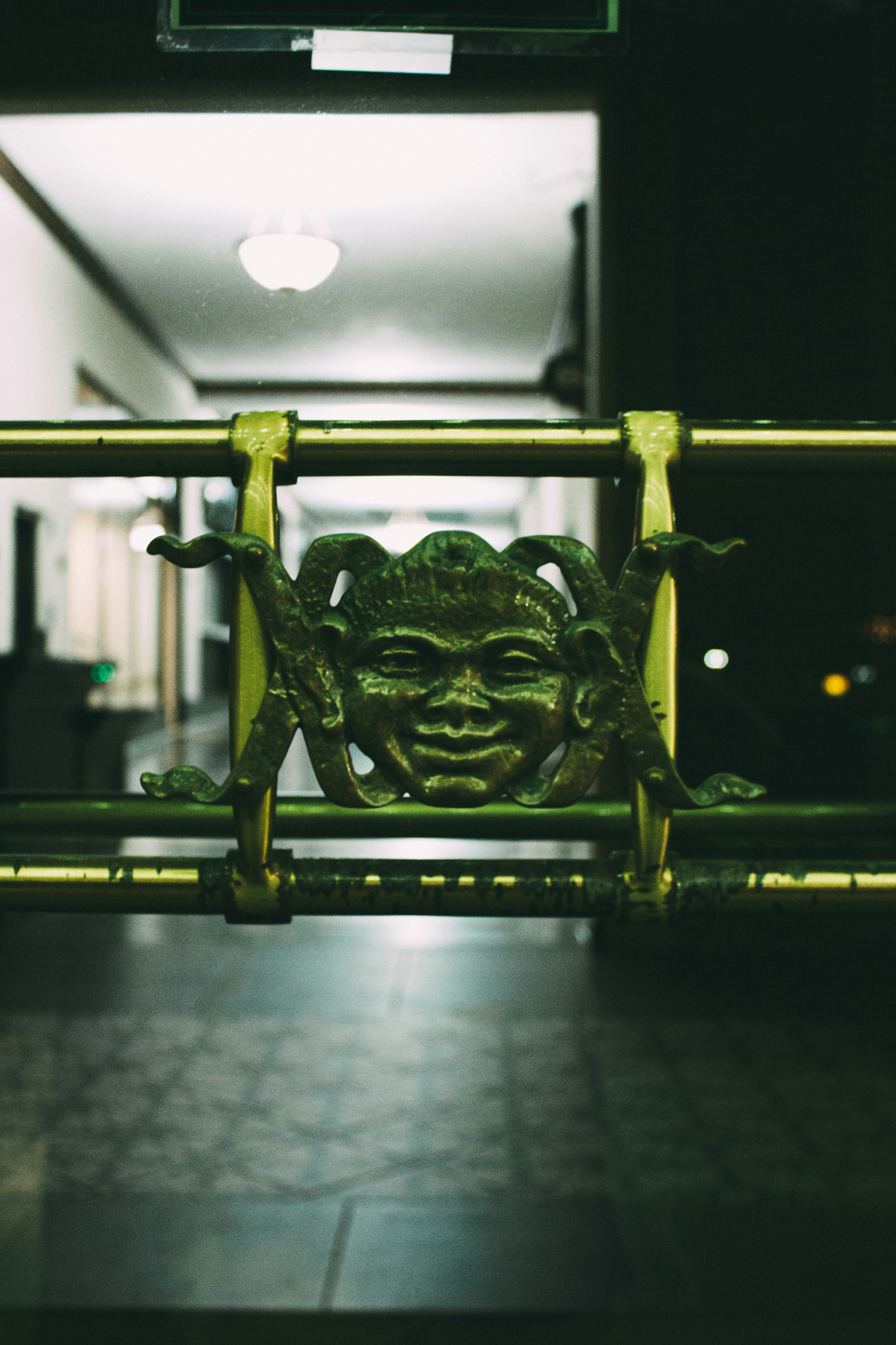 Intricate metalwork featuring a face motif, framed by a decorative railing in a dimly lit corridor.