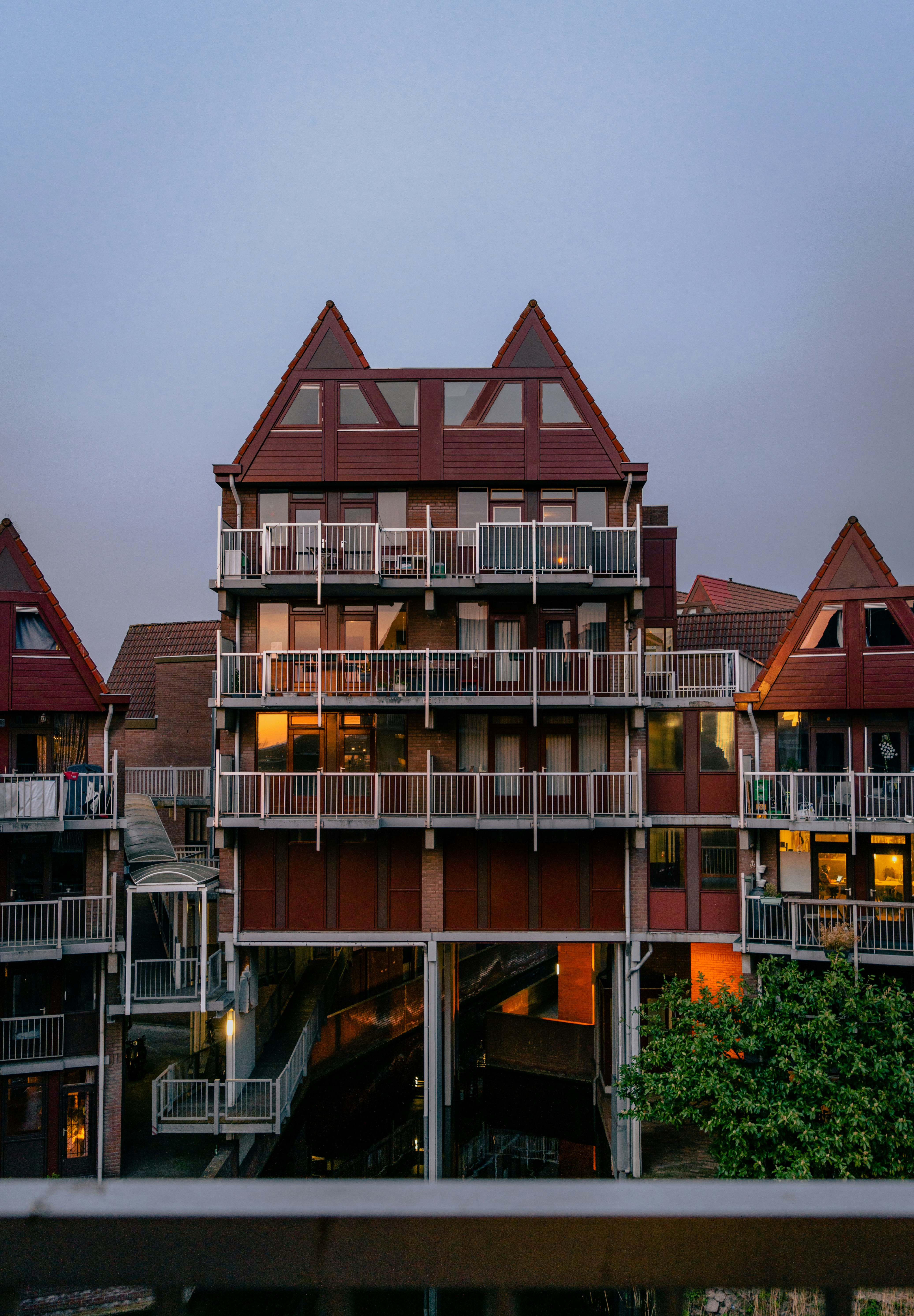Unique multi-story buildings with distinct triangular roofs, illuminated balconies, and lush greenery in the foreground.