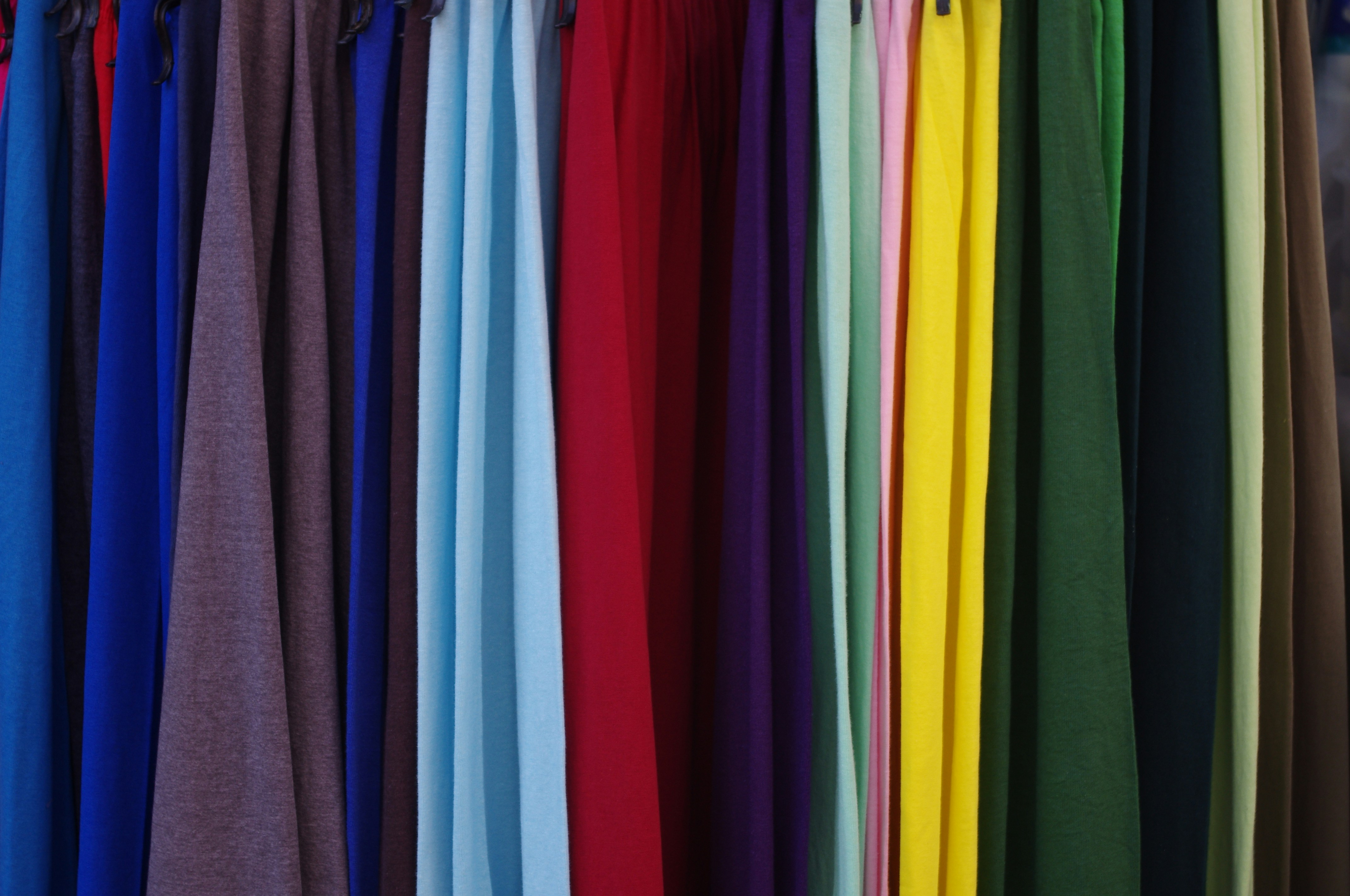 A vibrant array of hanging fabrics in various colors, showcasing different textures and shades. The collection highlights the diversity in textile design.