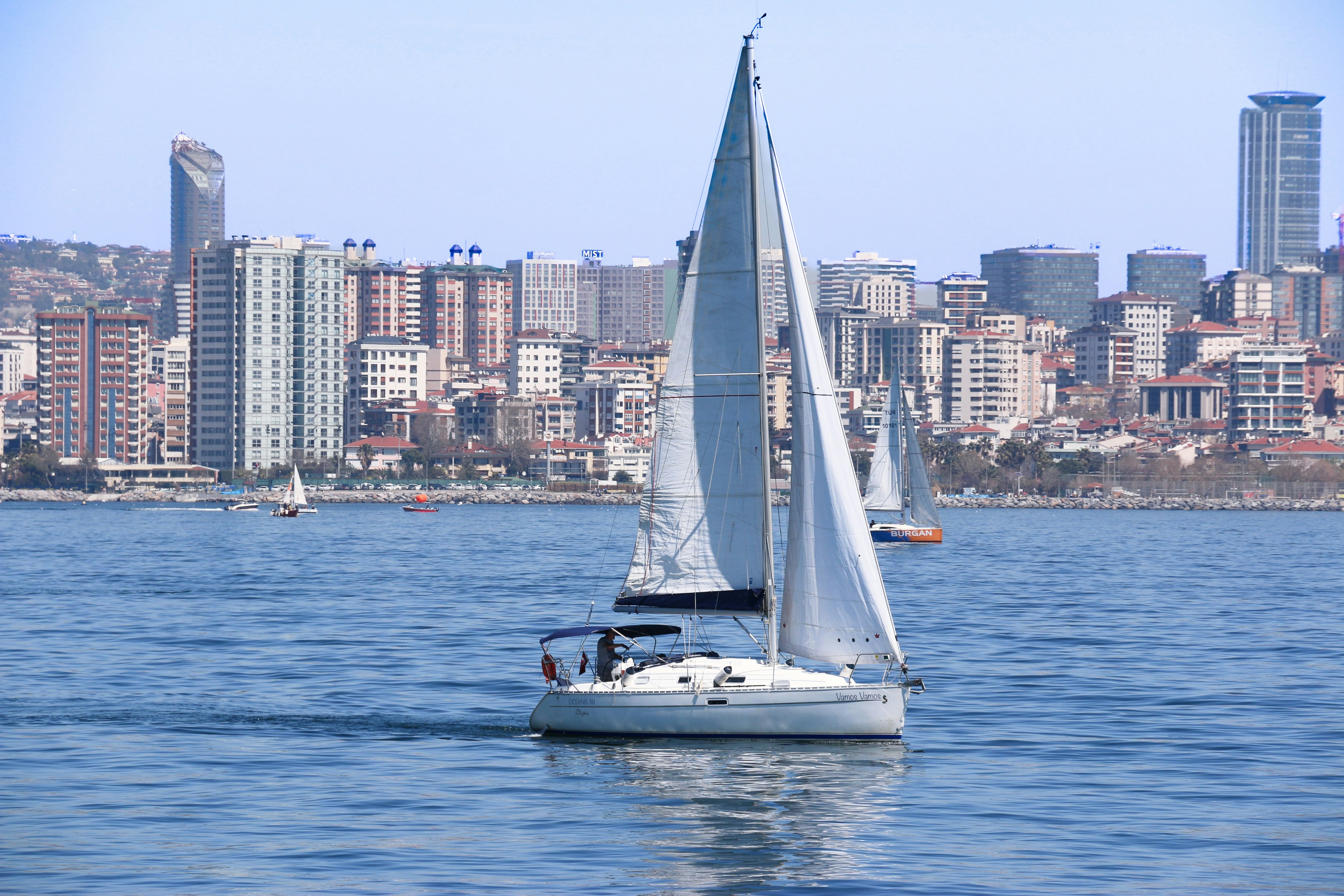 Two-sailed Yacht Slicing a Quiet Bay with a City Horizon