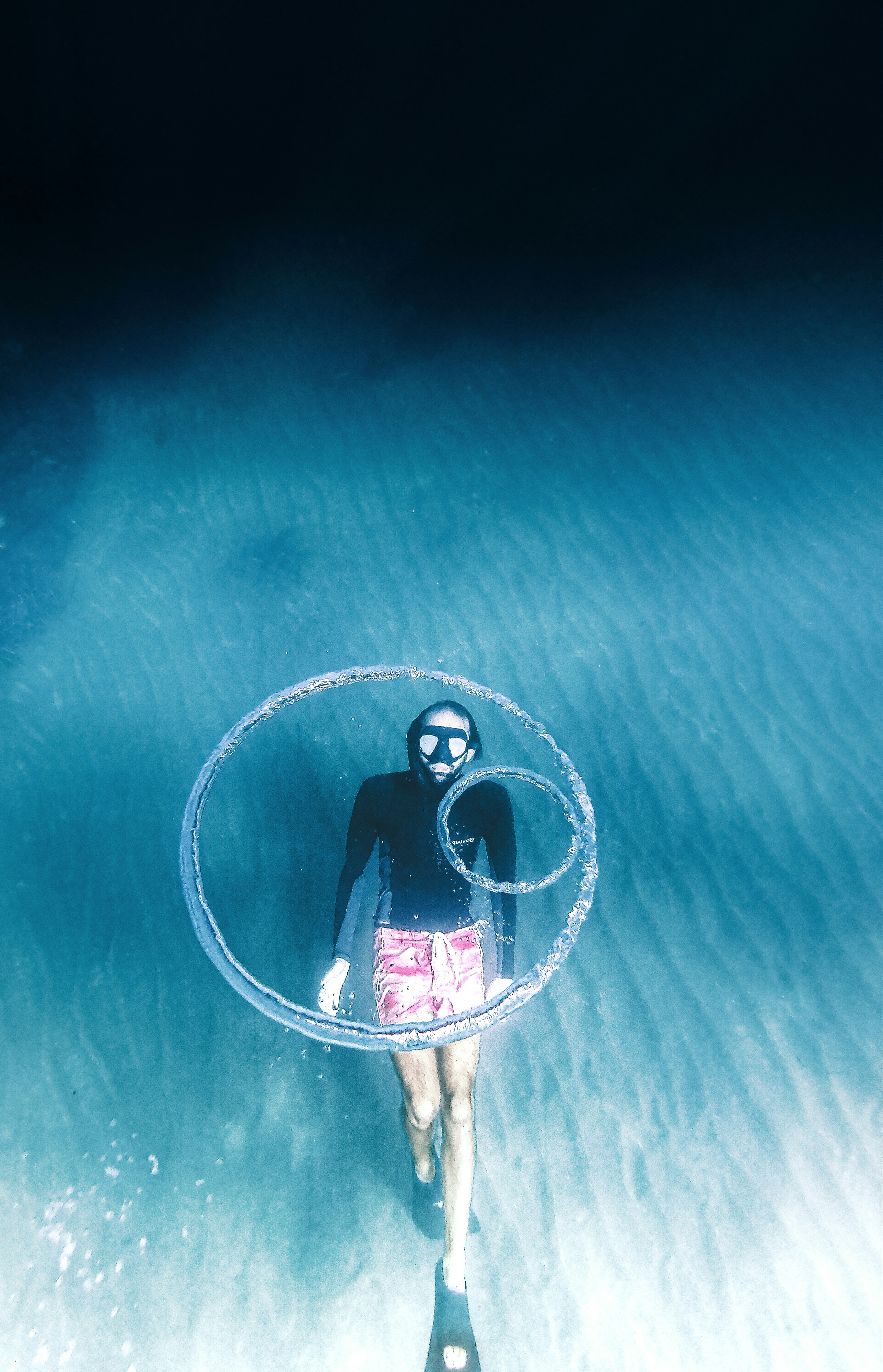 Rings of Motion: A Diver Drifts Through Two Circular Bubbles in Deep Blue