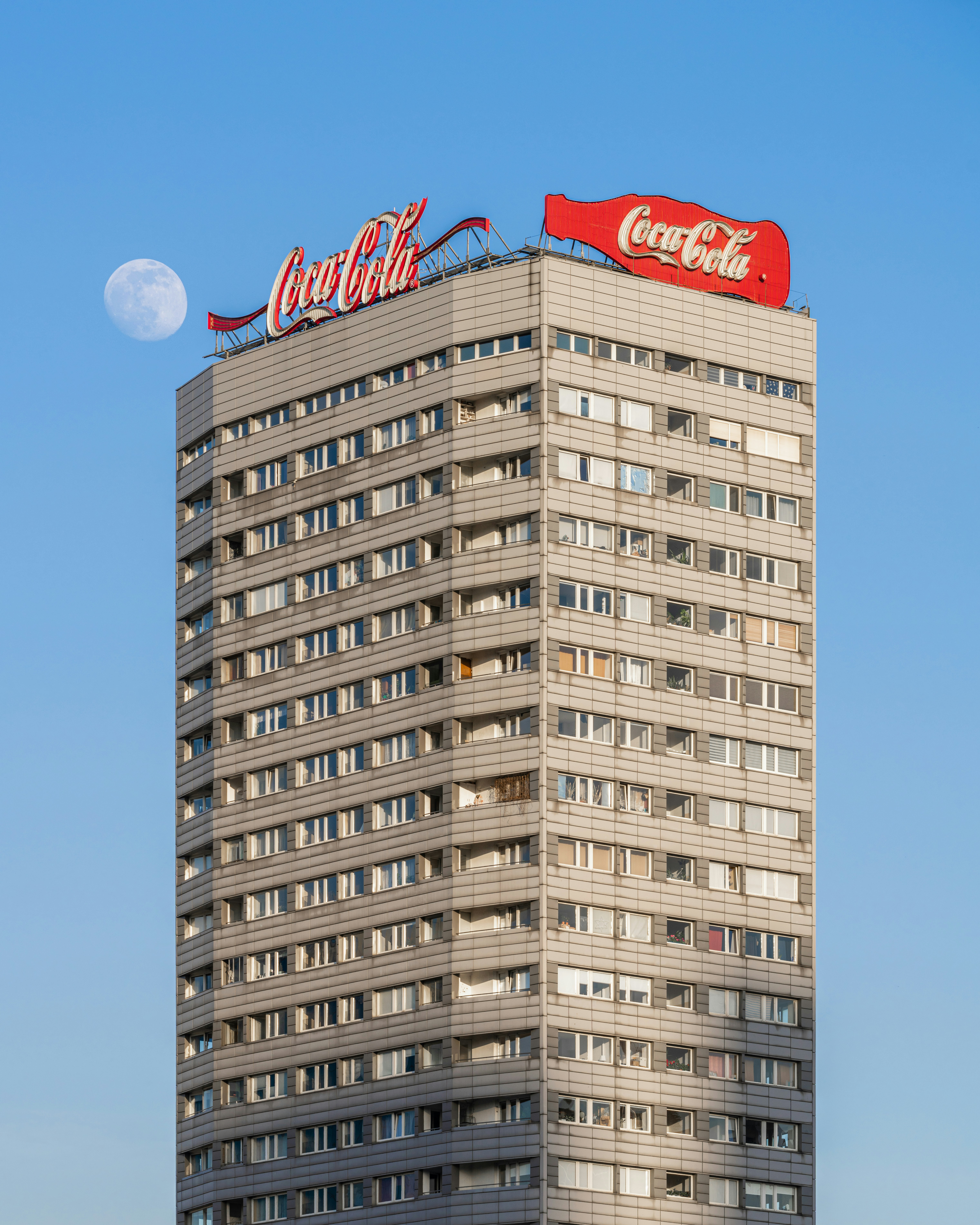 Coca-Cola Crest on a Sky-Blue High-Rise Under a Crescent Moon