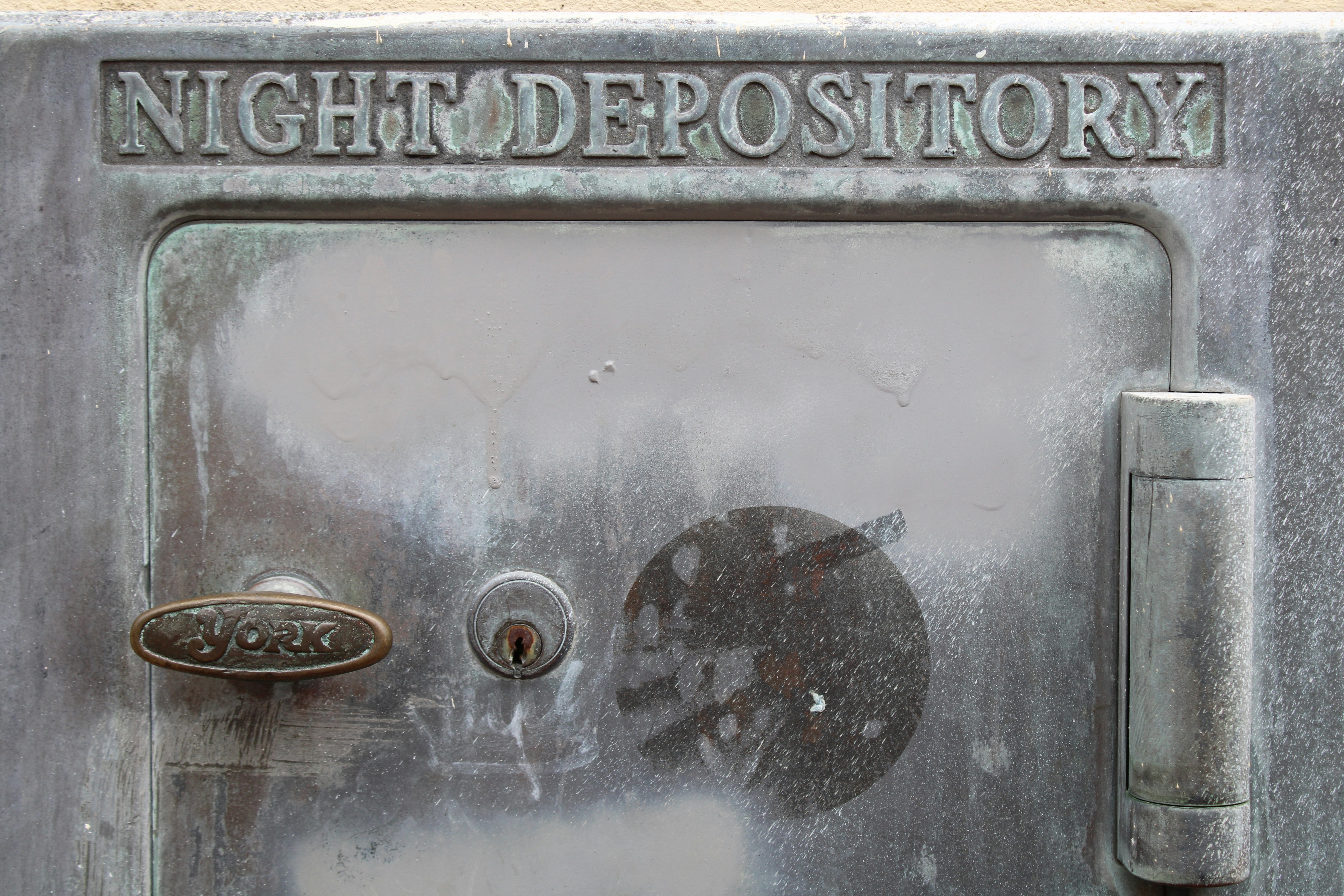 Weathered night depository with a prominent lock and faded lettering, showcasing urban history and security features.