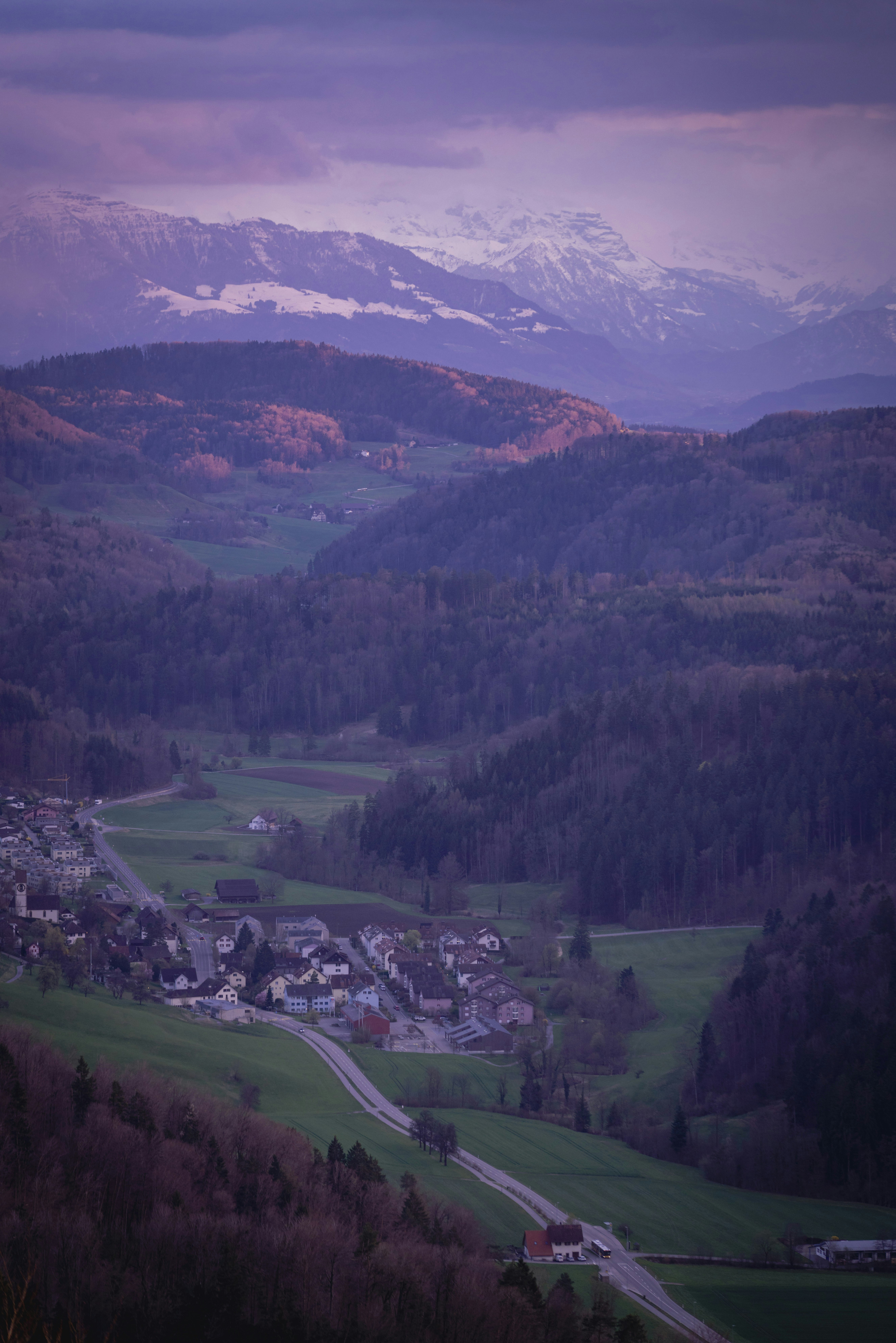 Serene landscape showcasing a quaint village nestled in a lush valley, surrounded by majestic mountains under a twilight sky.