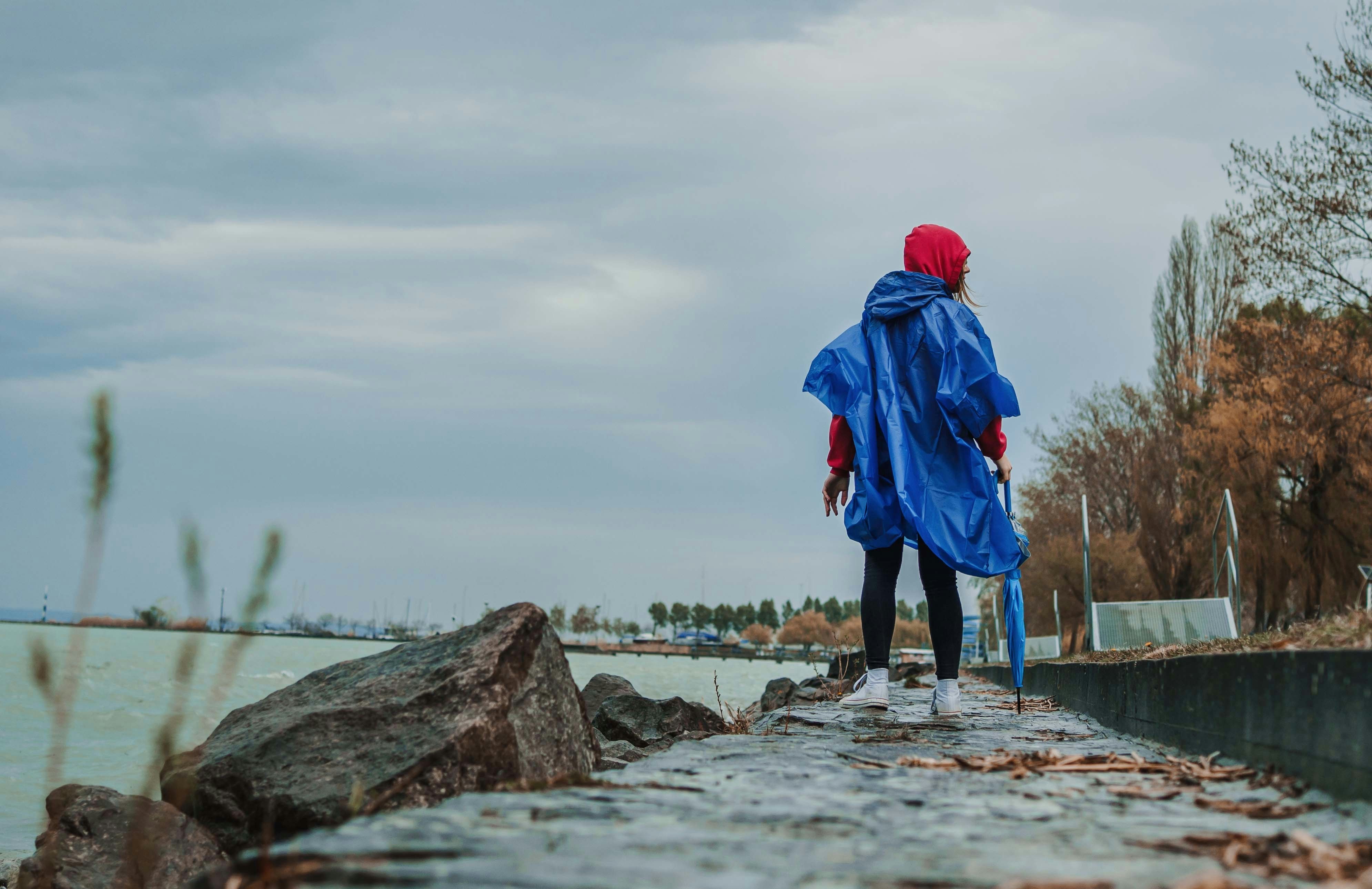 Foto Una persona con un impermeable azul de pie en un muelle – Imagen ...