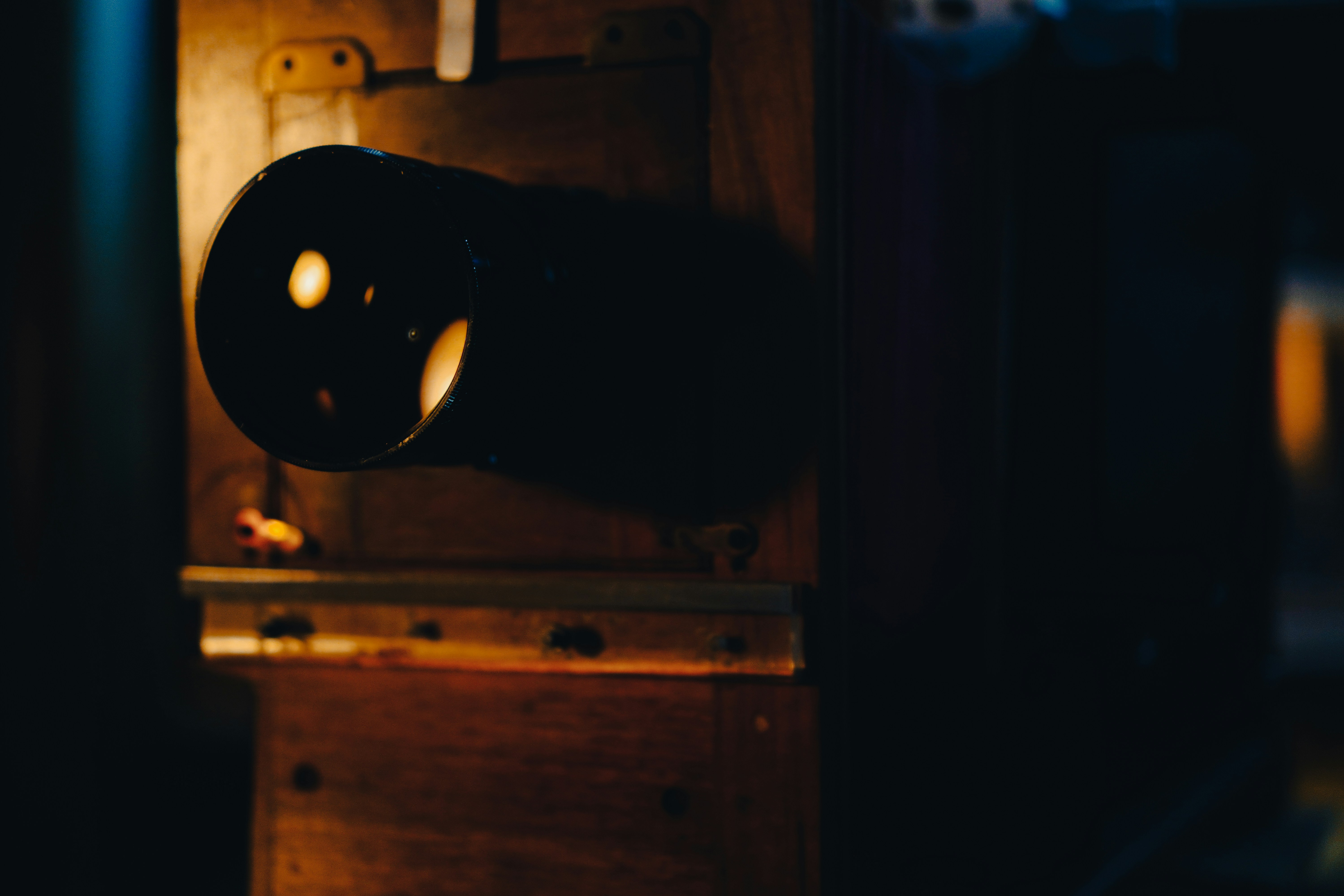 Close-up of a vintage camera lens mounted on a wooden body, illuminated by soft ambient light.