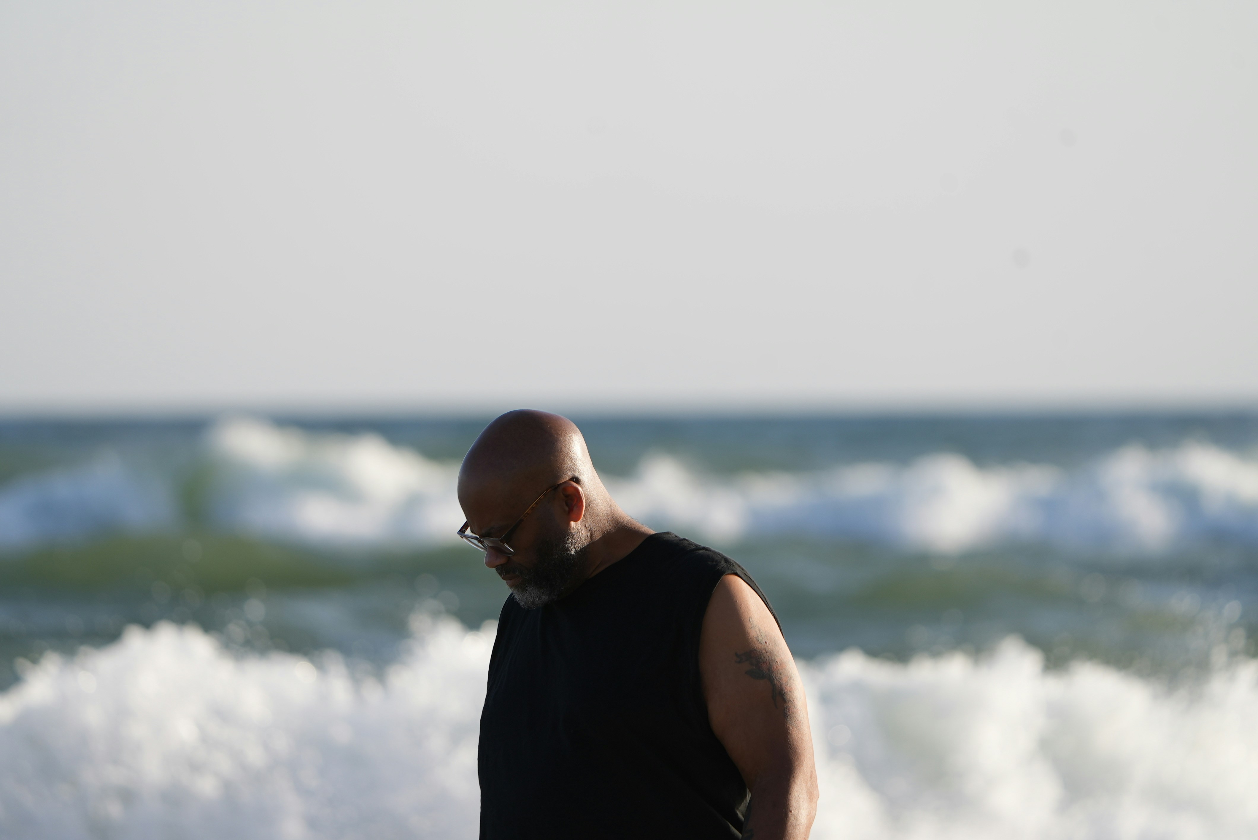 A bald man standing on a beach next to the ocean photo – Free Human ...
