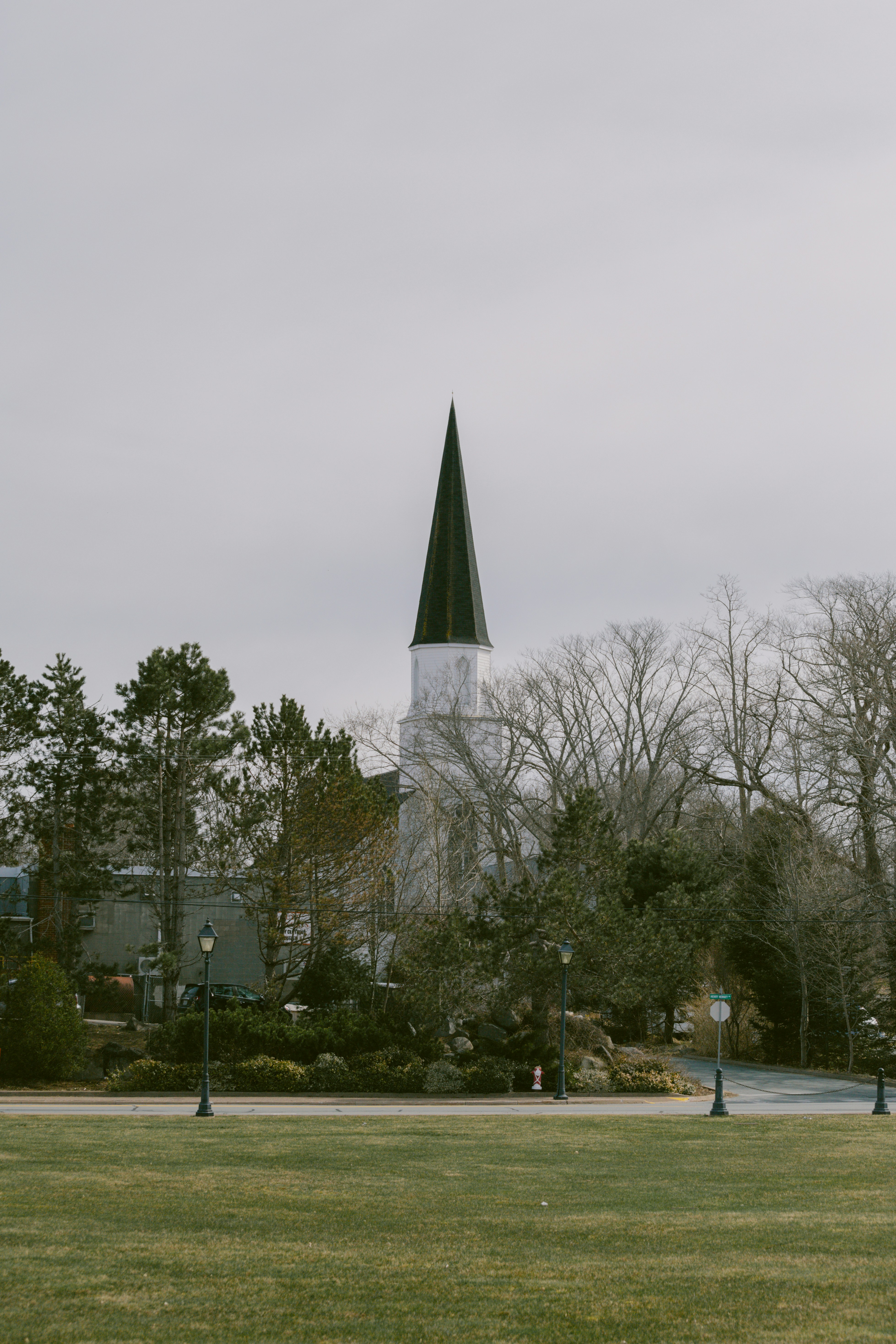 A tall church steeple rises prominently amidst a backdrop of bare trees and overcast skies, hinting at a tranquil yet somber atmosphere.