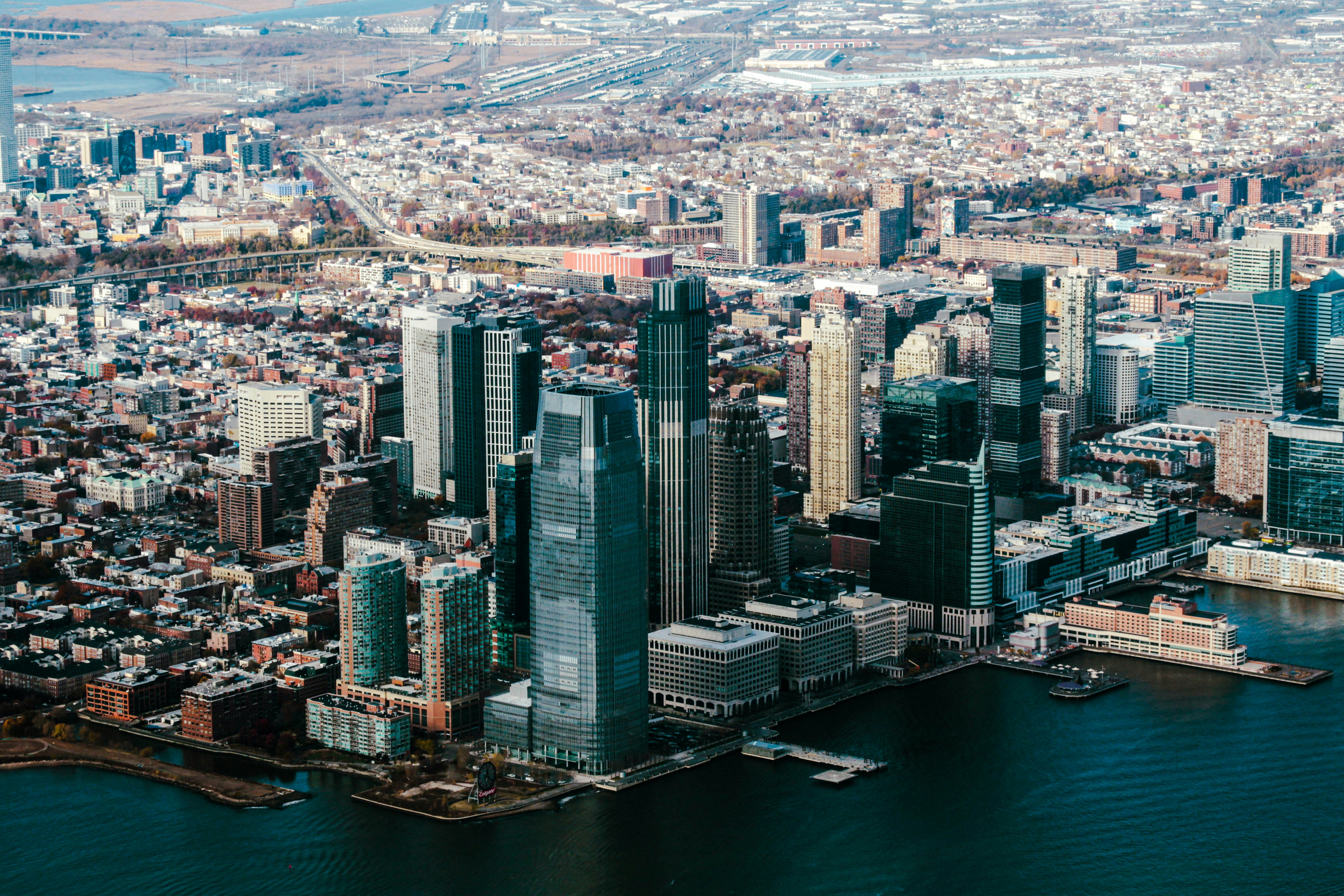 Aerial view of a sprawling cityscape with towering skyscrapers adjacent to a wide river under a clear sky.