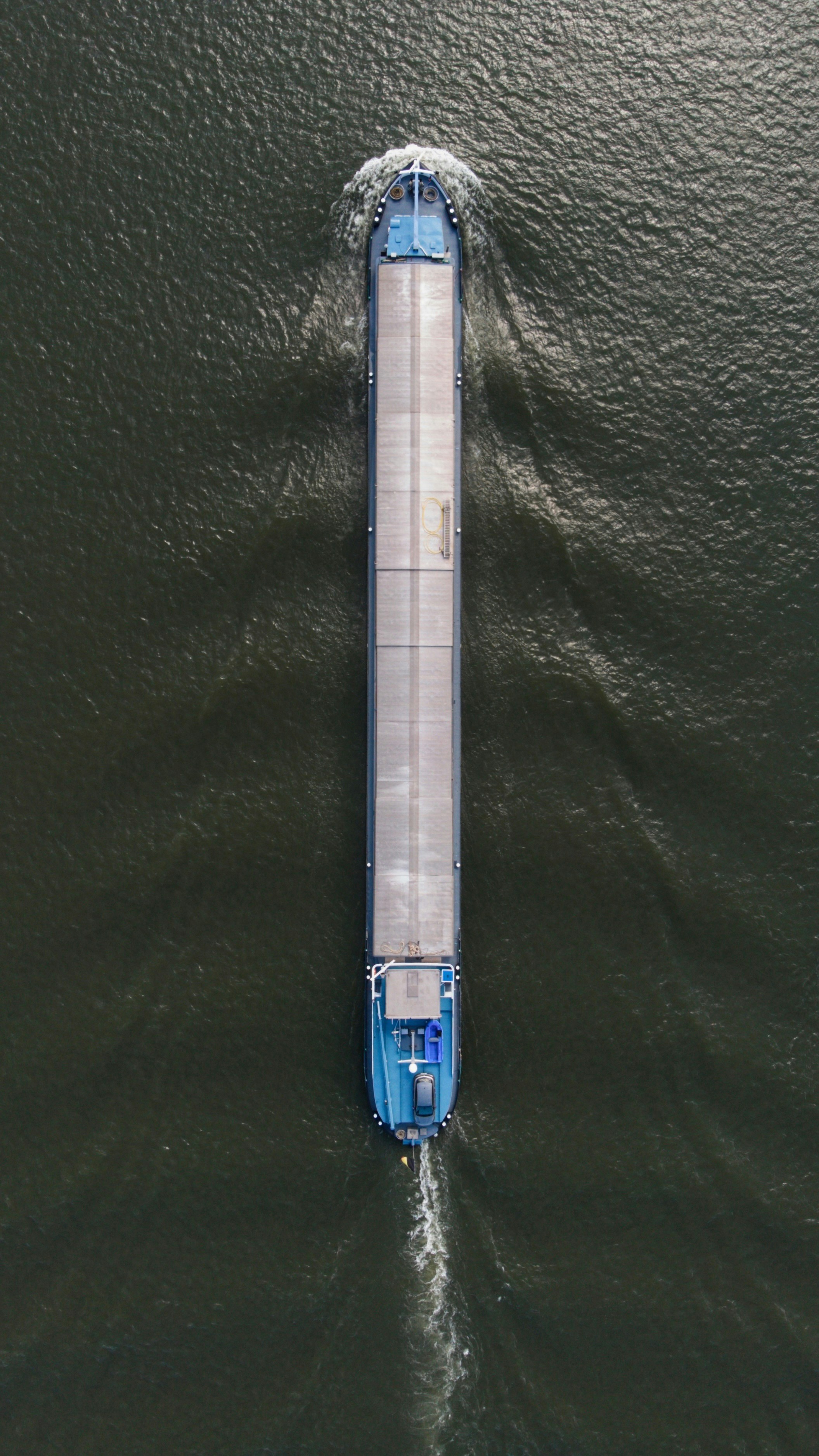 Aerial view of a large cargo ship gliding through dark waters, showcasing its streamlined design and wake patterns.